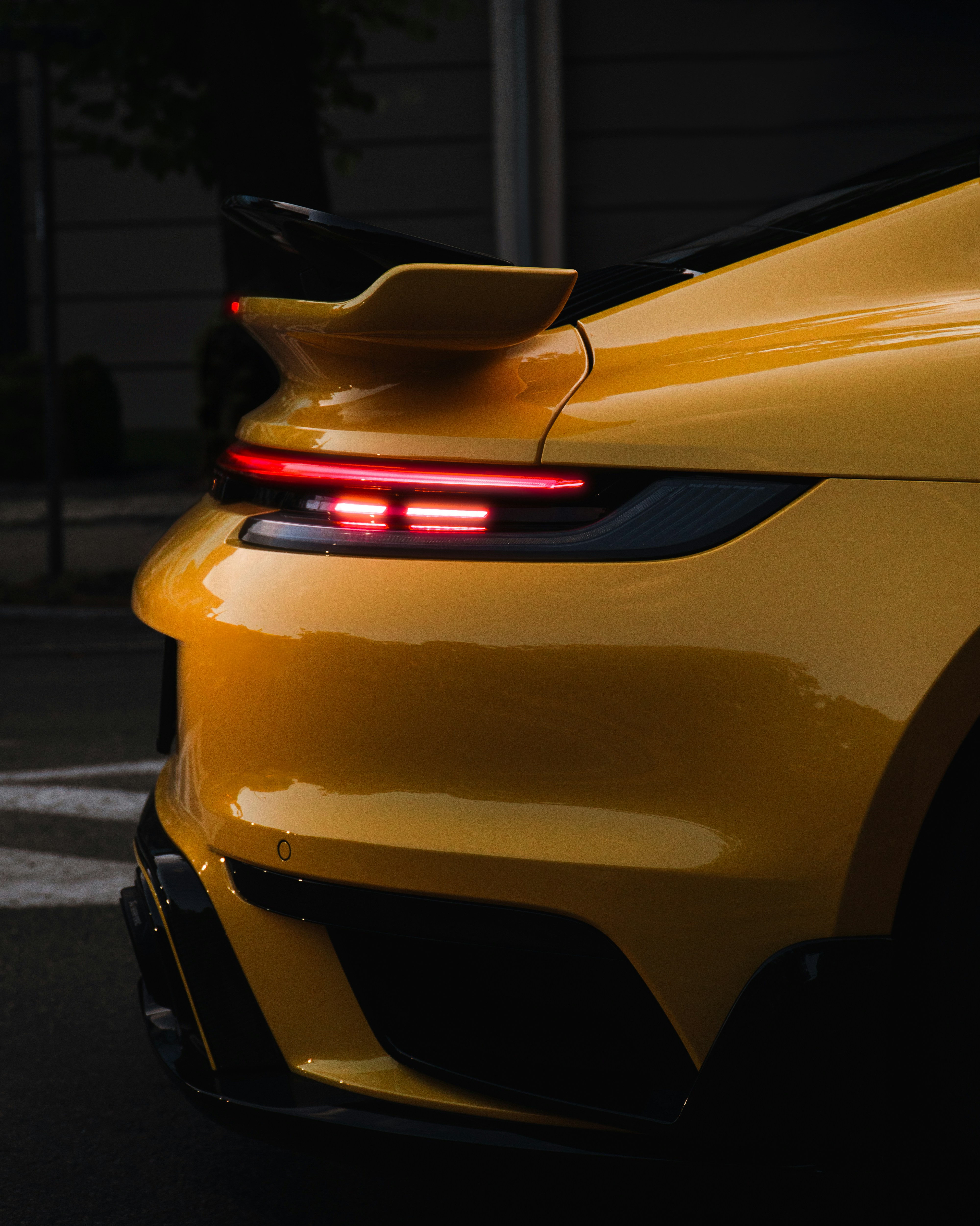 Rear spoiler silhouette and taillight glow on a yellow sports car
