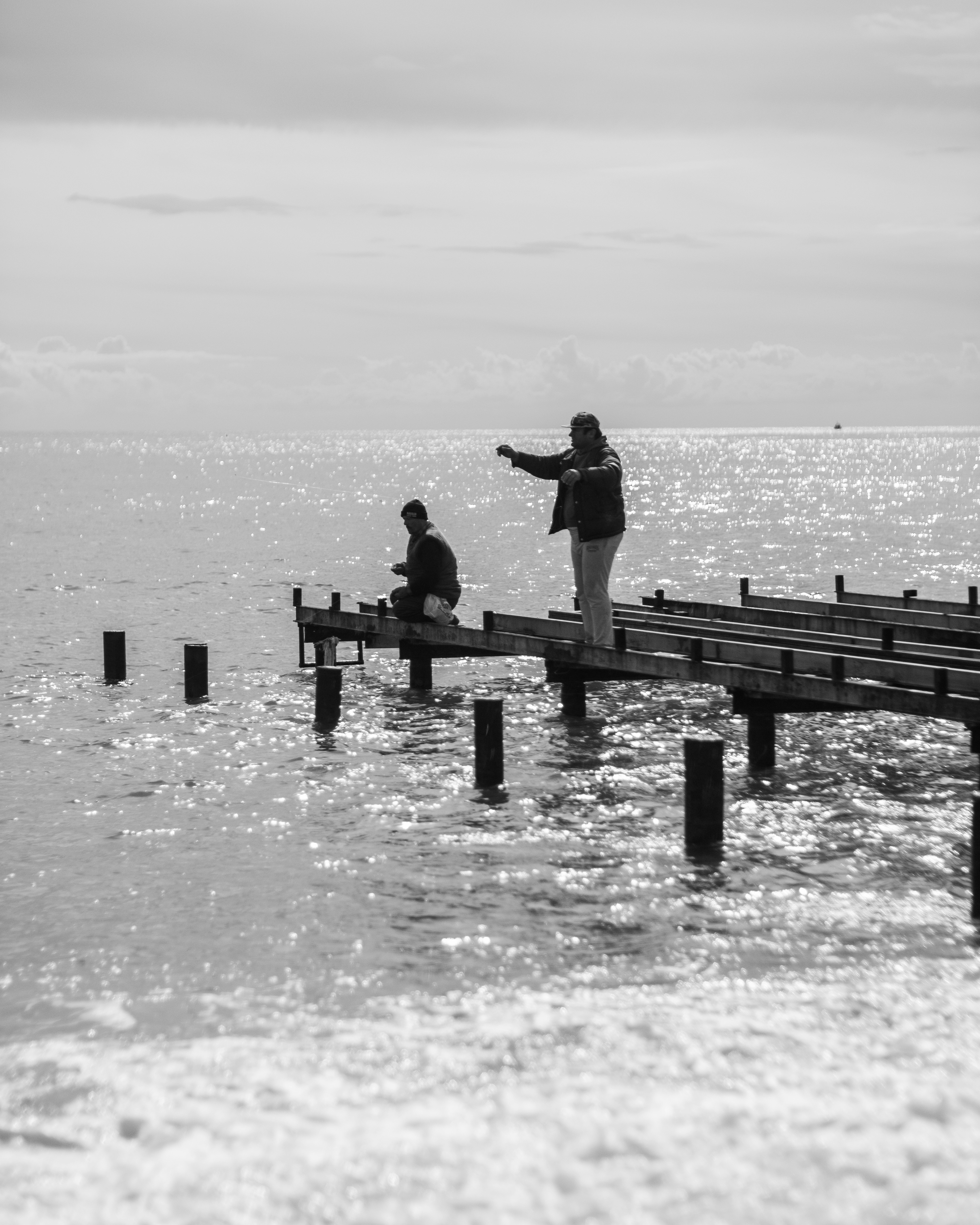 Figures on a Quiet Pier: A Silver-Glinted Moment by the Sea