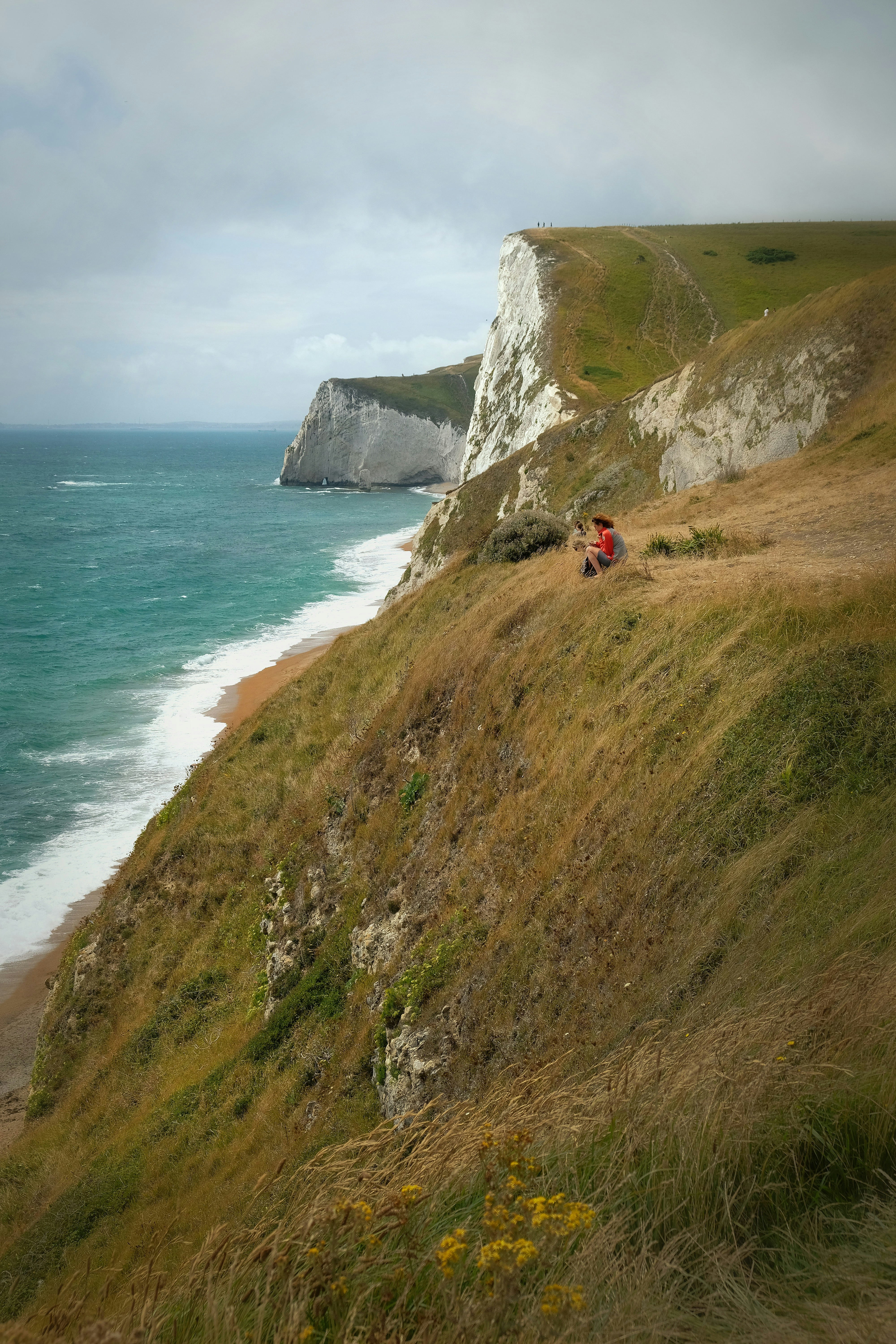On the Edge: A Hiker Resting Against Green Cliffs Over the Turquoise Sea