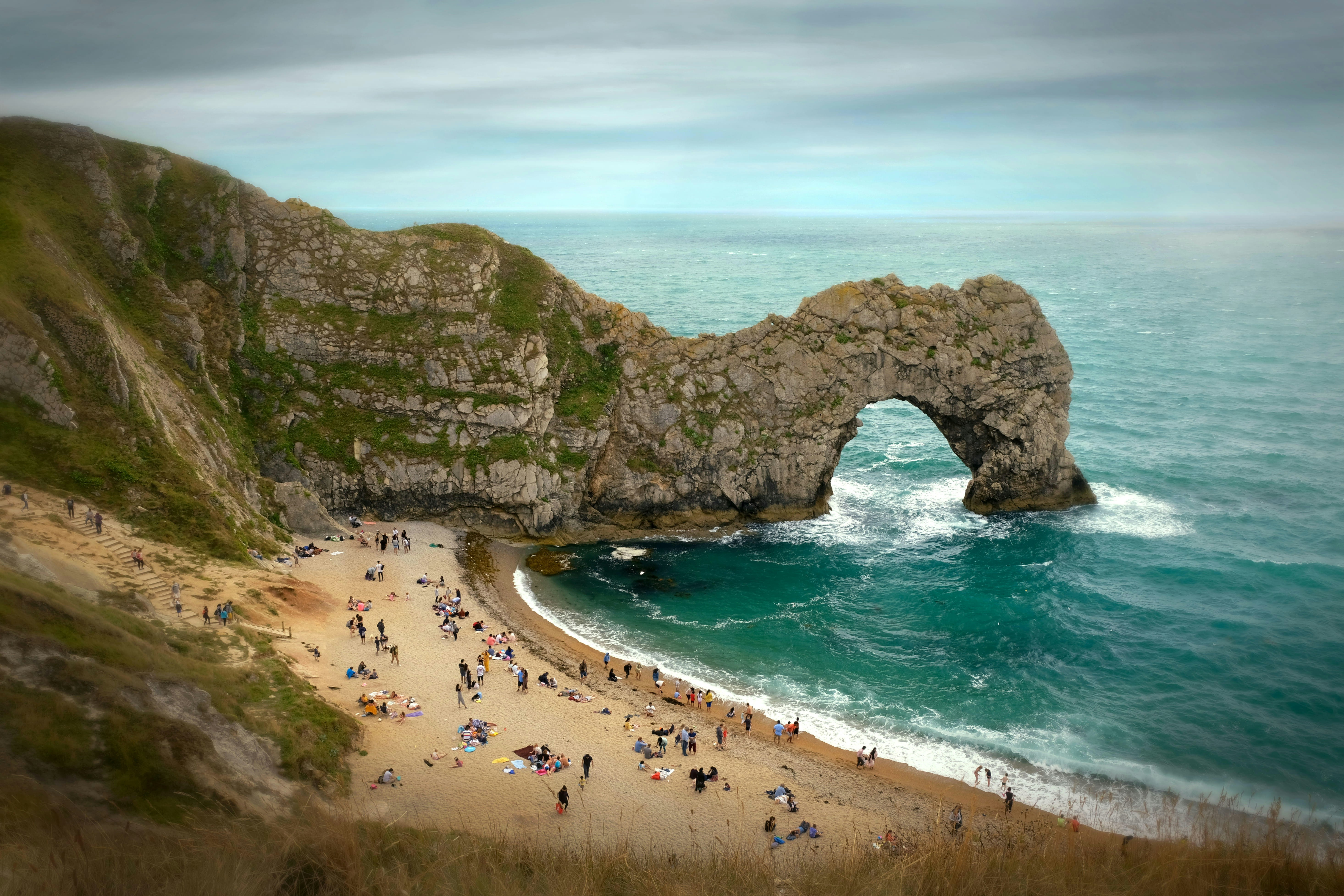 Sea Arch at Dusk: People on the sandy cove beneath the cliff