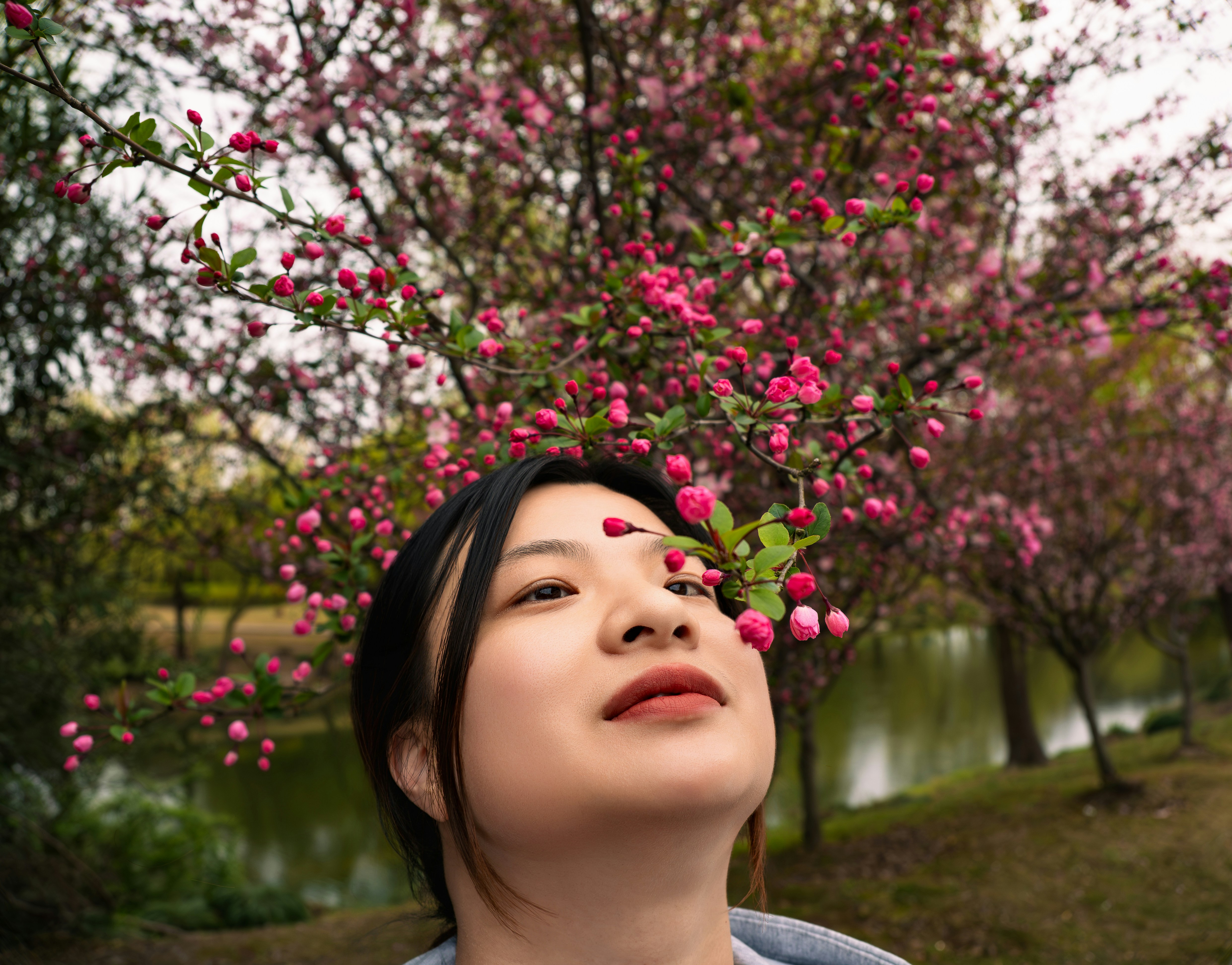 Young woman smelling pink blossoms near a lake