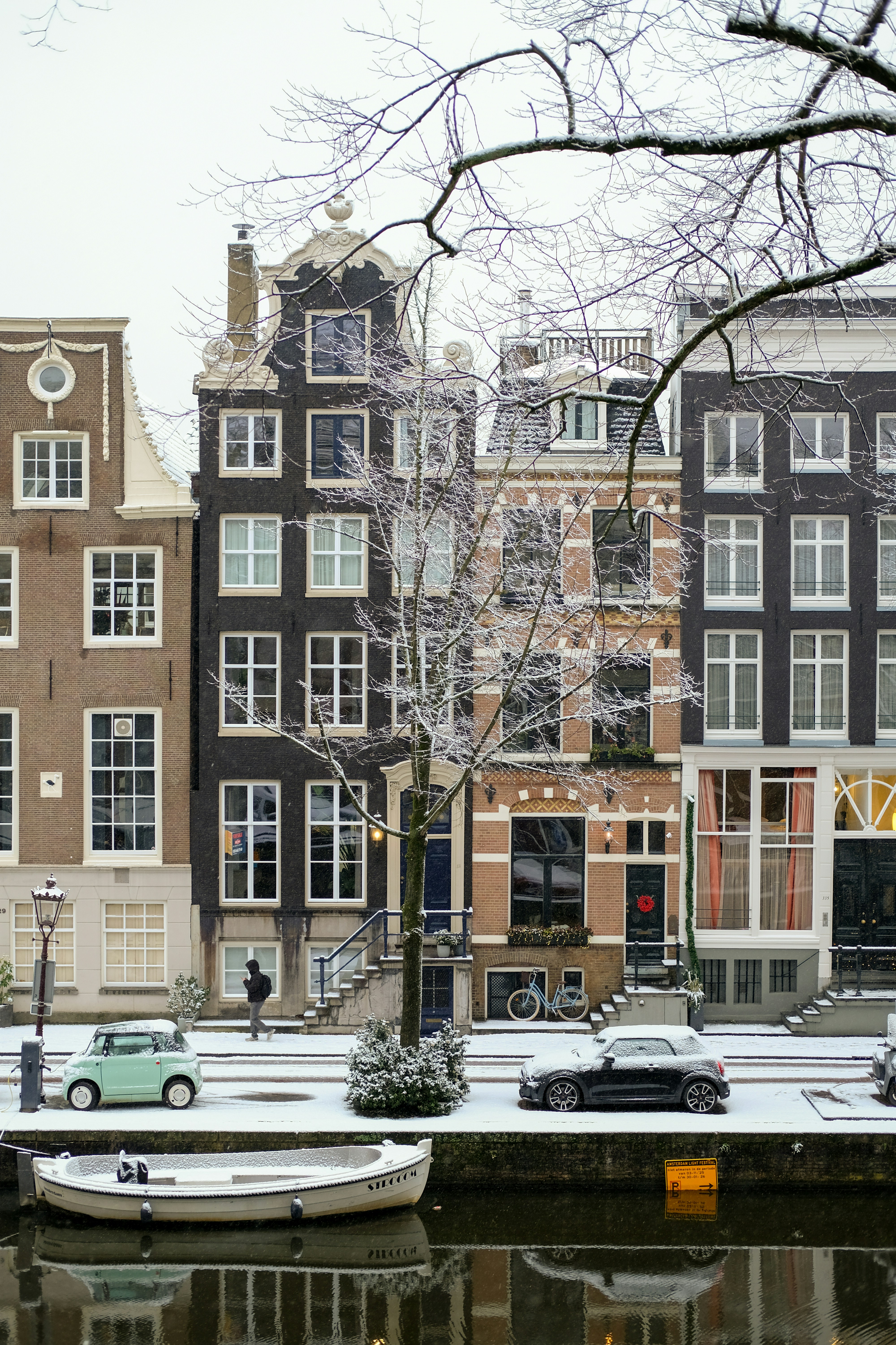 Snow-dusted canal street framed by stepped façades of Amsterdam-style townhouses