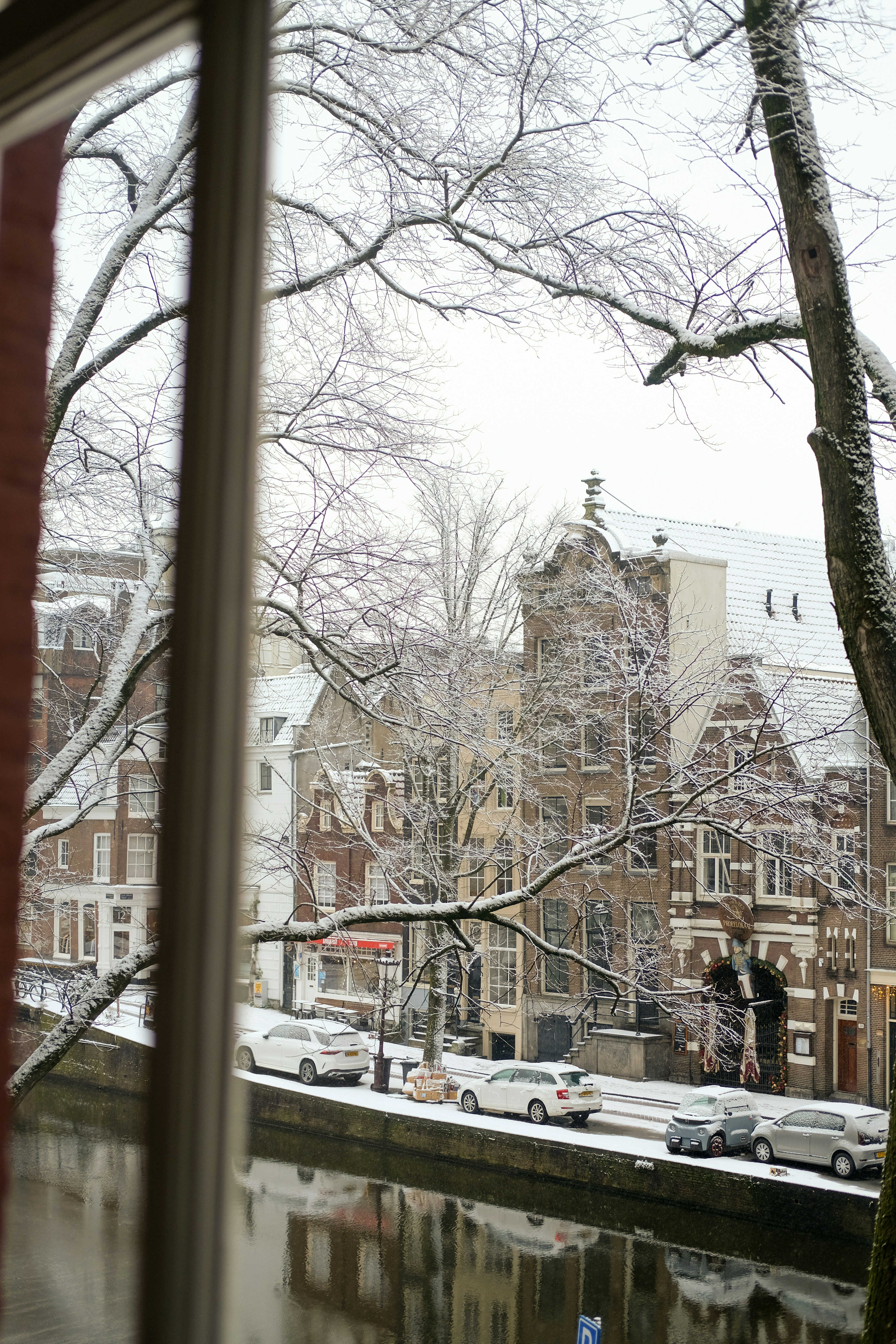 Snow-blanketed urban canal from a warm interior window