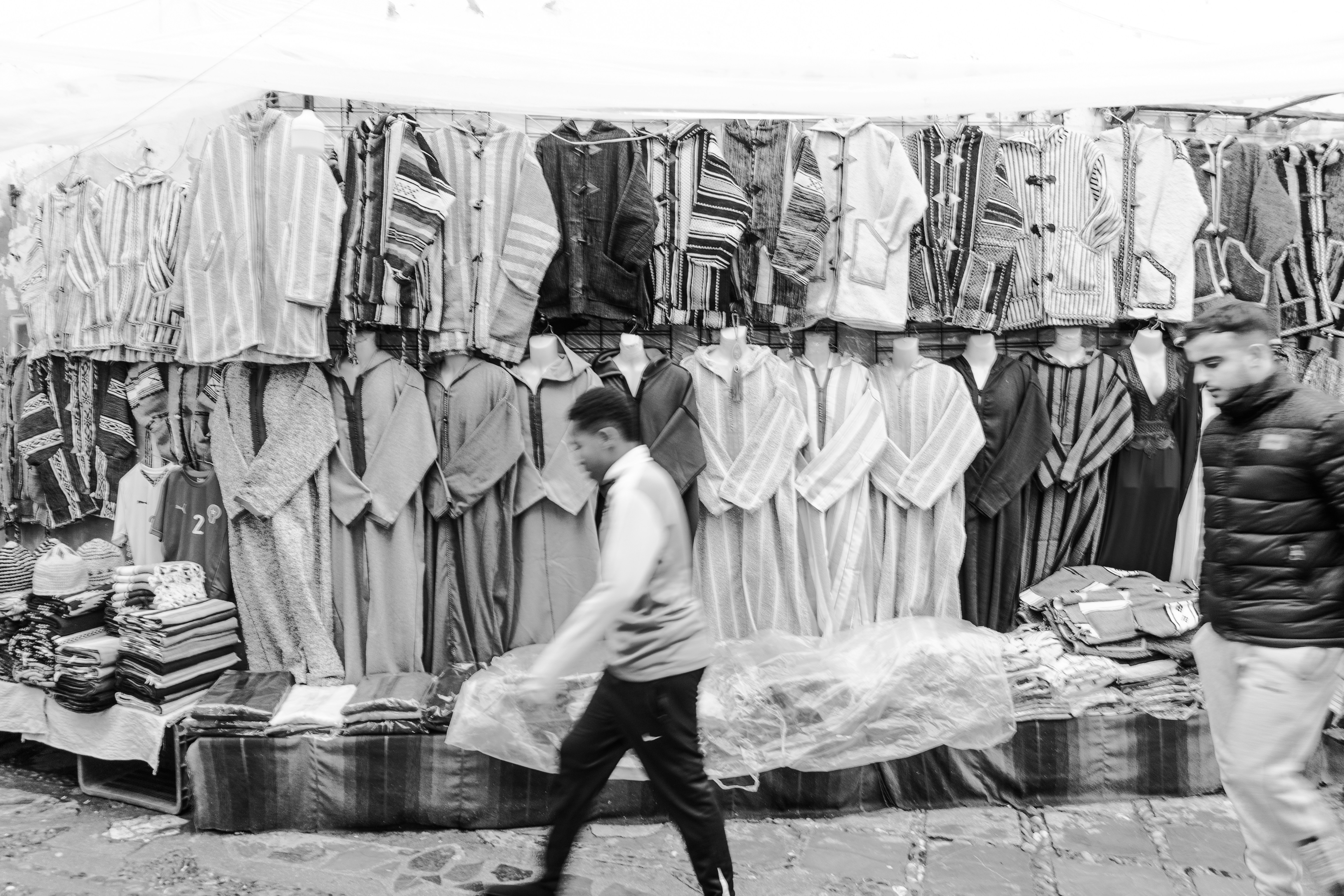 Market Frieze: Stacked Garments and Passing Pedestrians