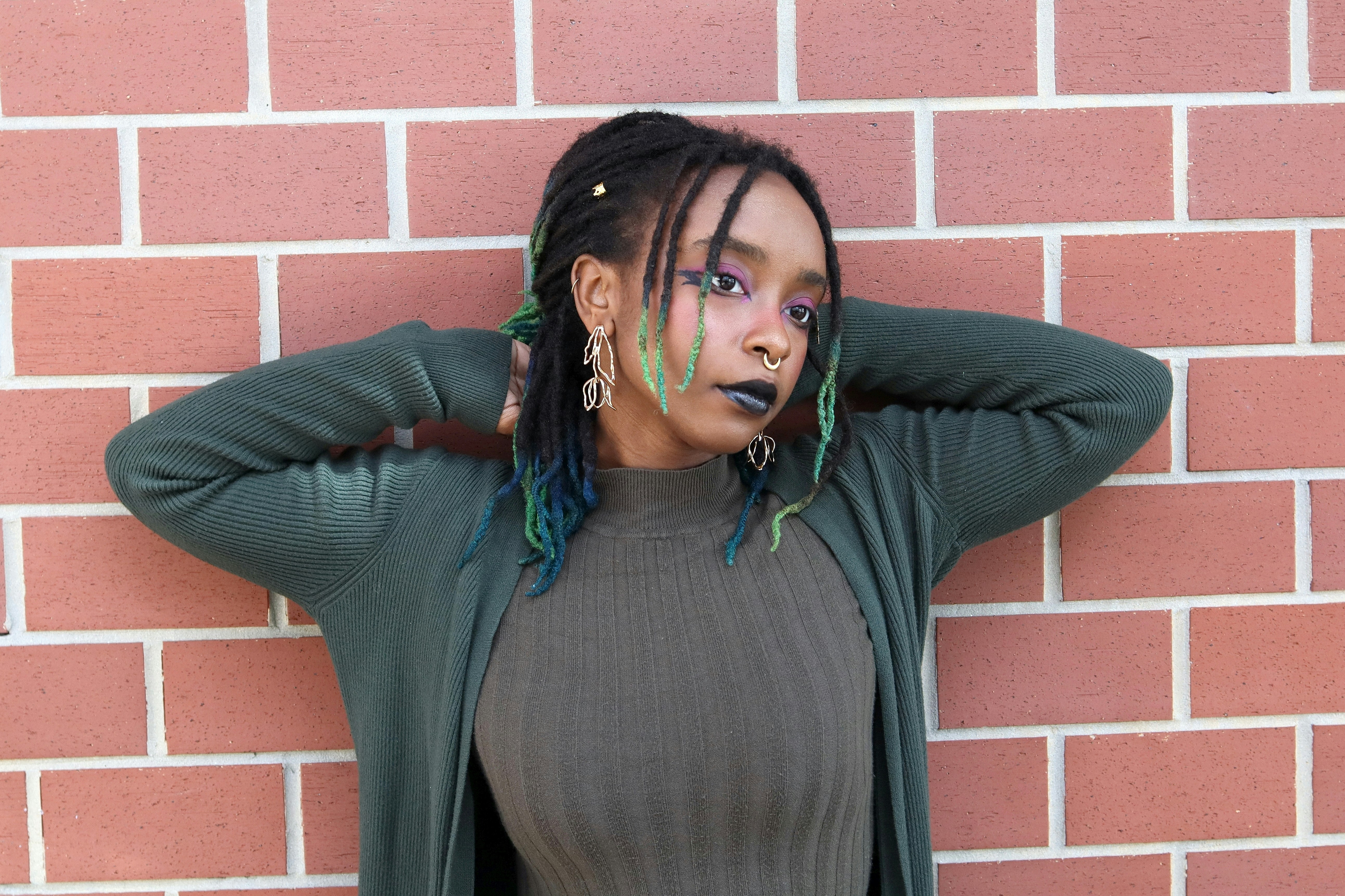 Colorful dreadlocks and confident stance against brick backdrop