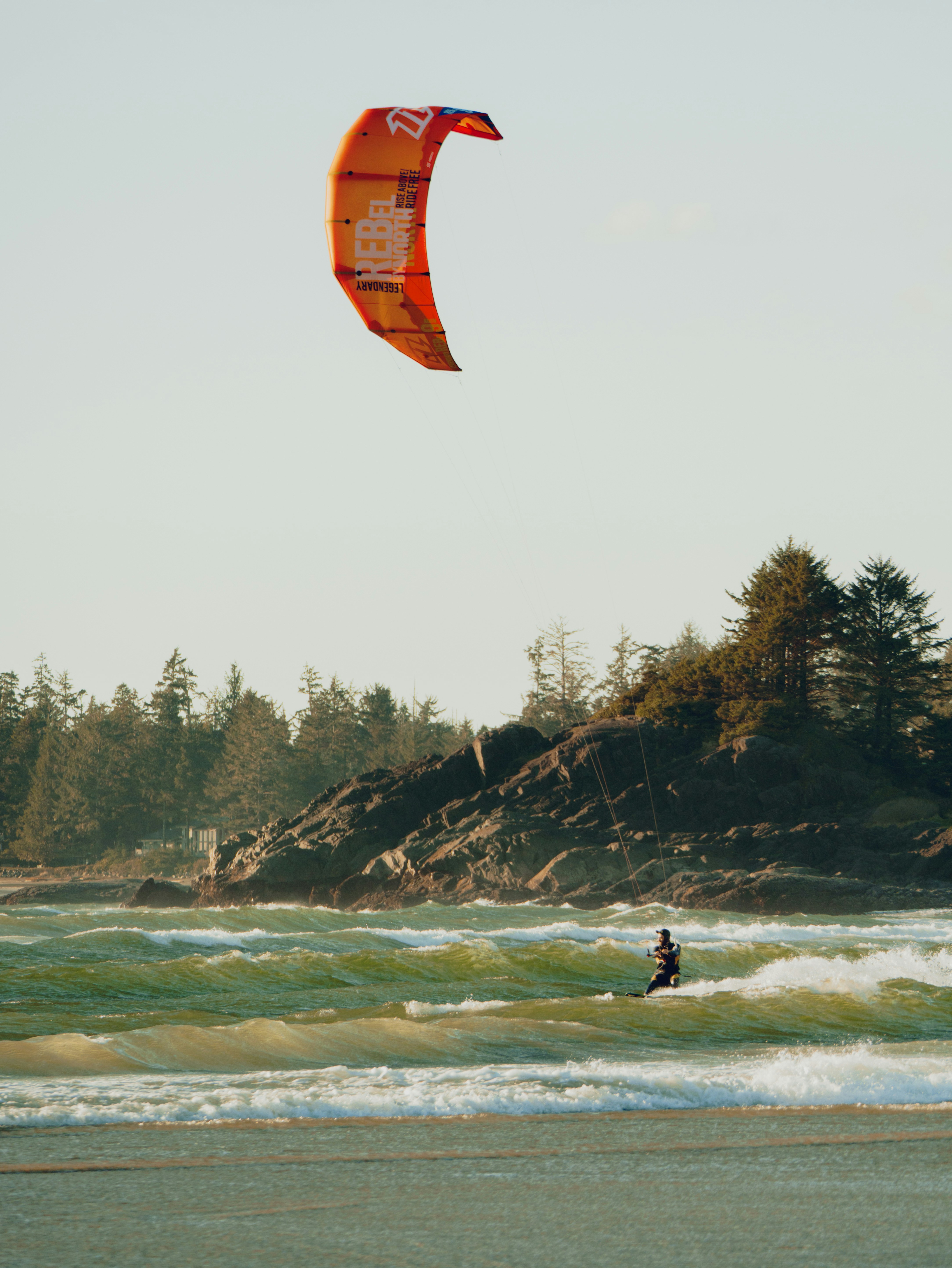 Kiteboarder riding a wave near a rocky shore.