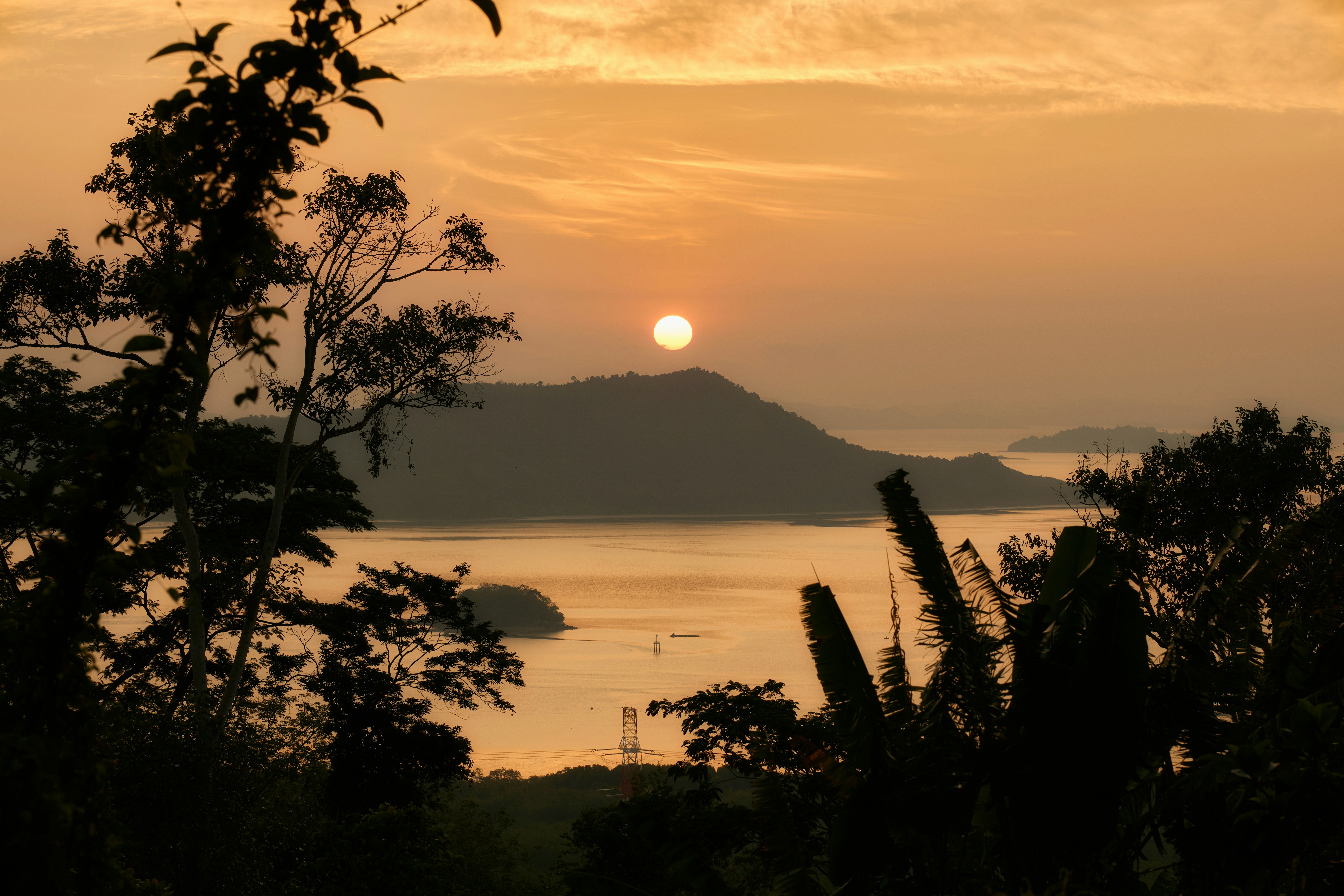 Sunset Over a Silhouette: Island Ridge Framed by Tropical Foliage