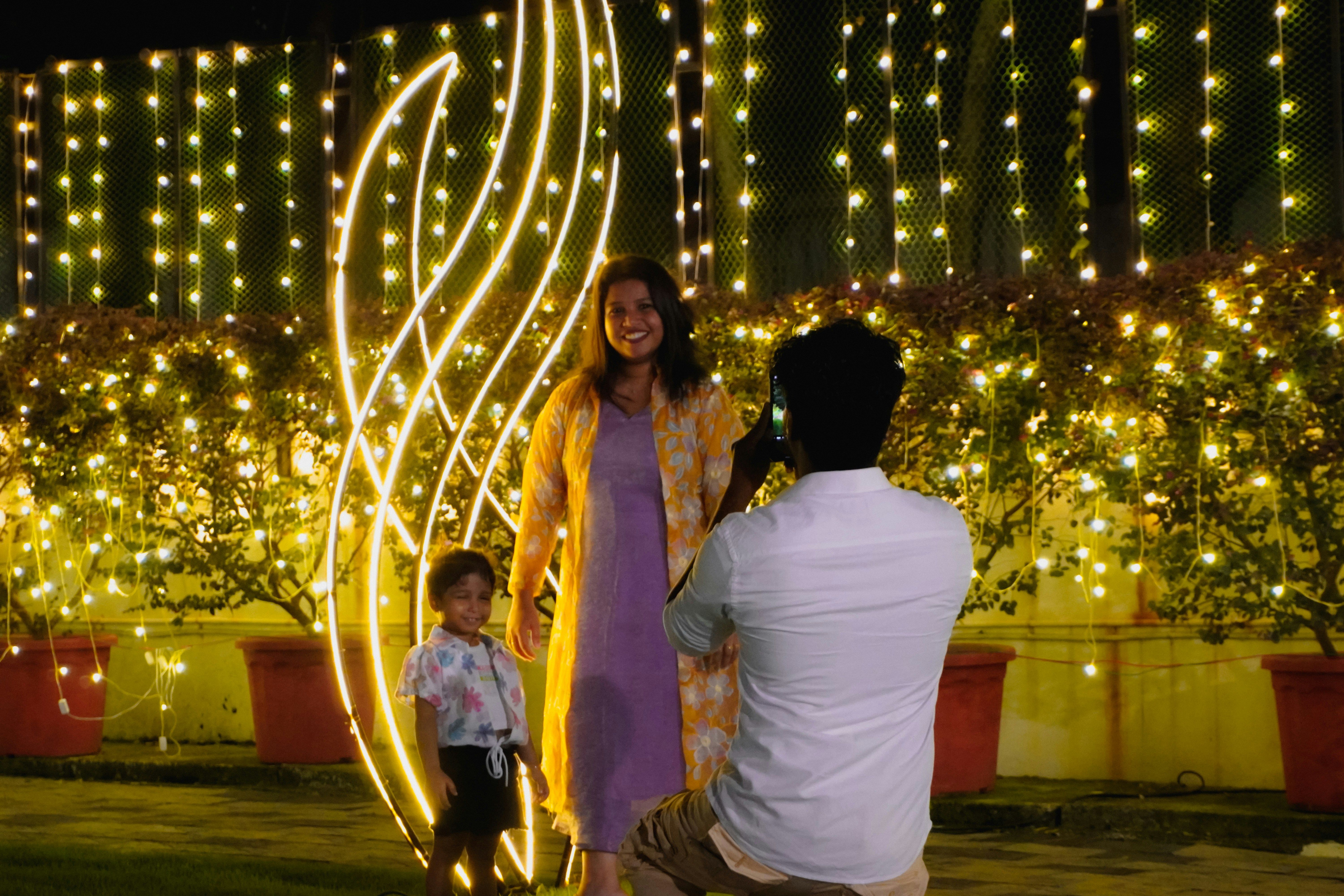Man photographs woman and child with festive lights