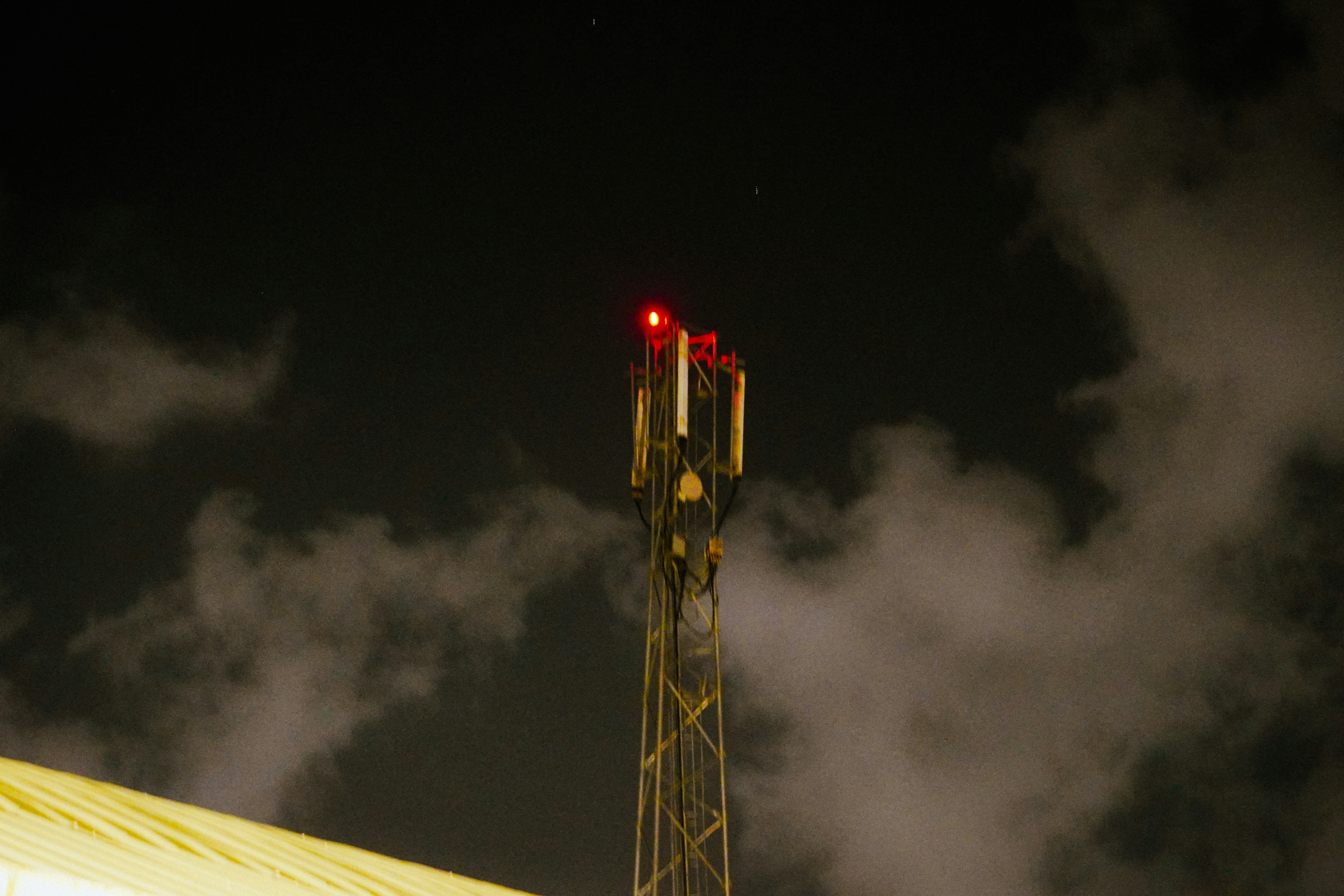 Red beacon above quiet night: a cellular tower silhouette against drifting clouds