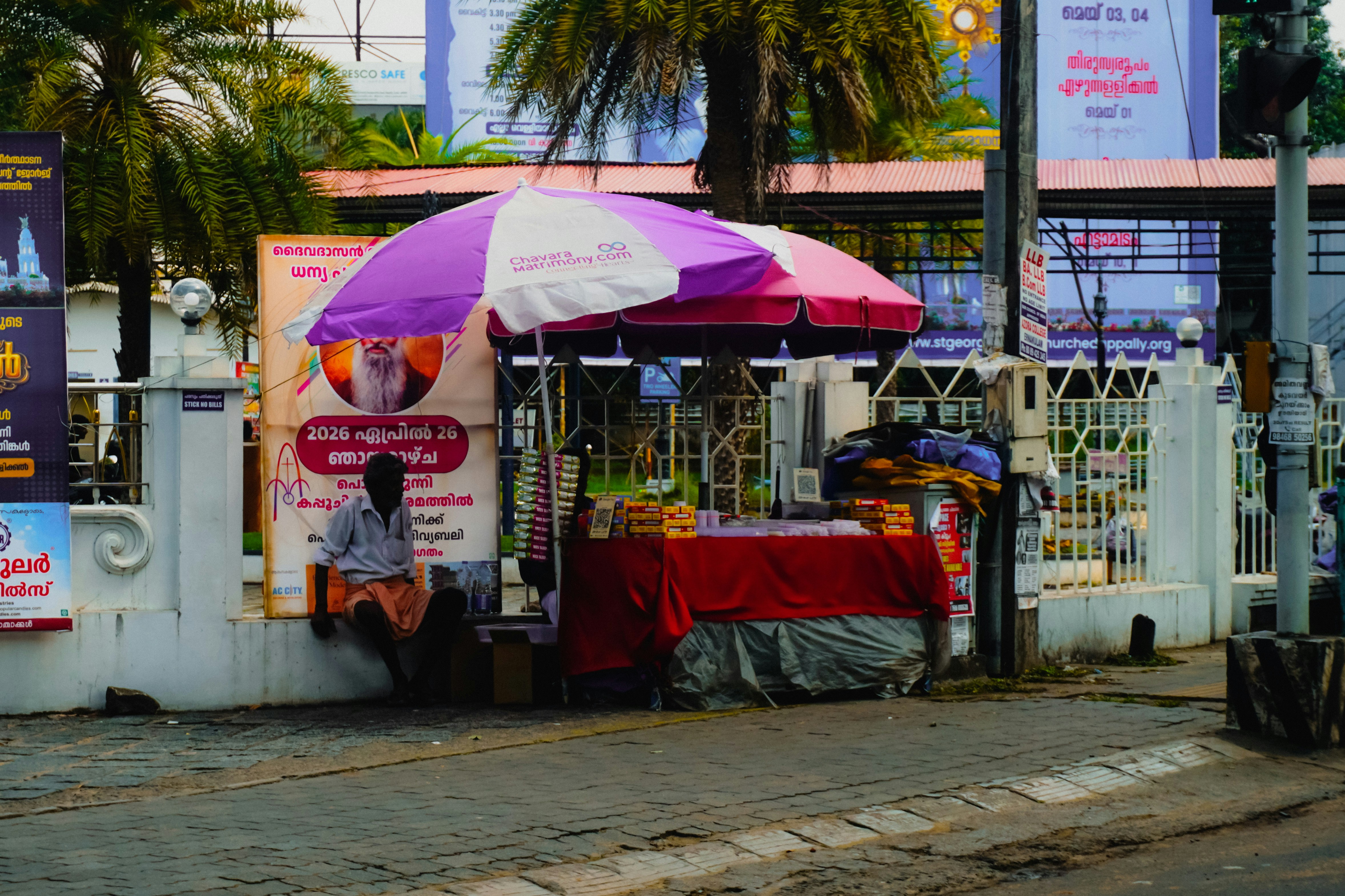 Market Stall Under a Purple-White Umbrella in a Sunny Street