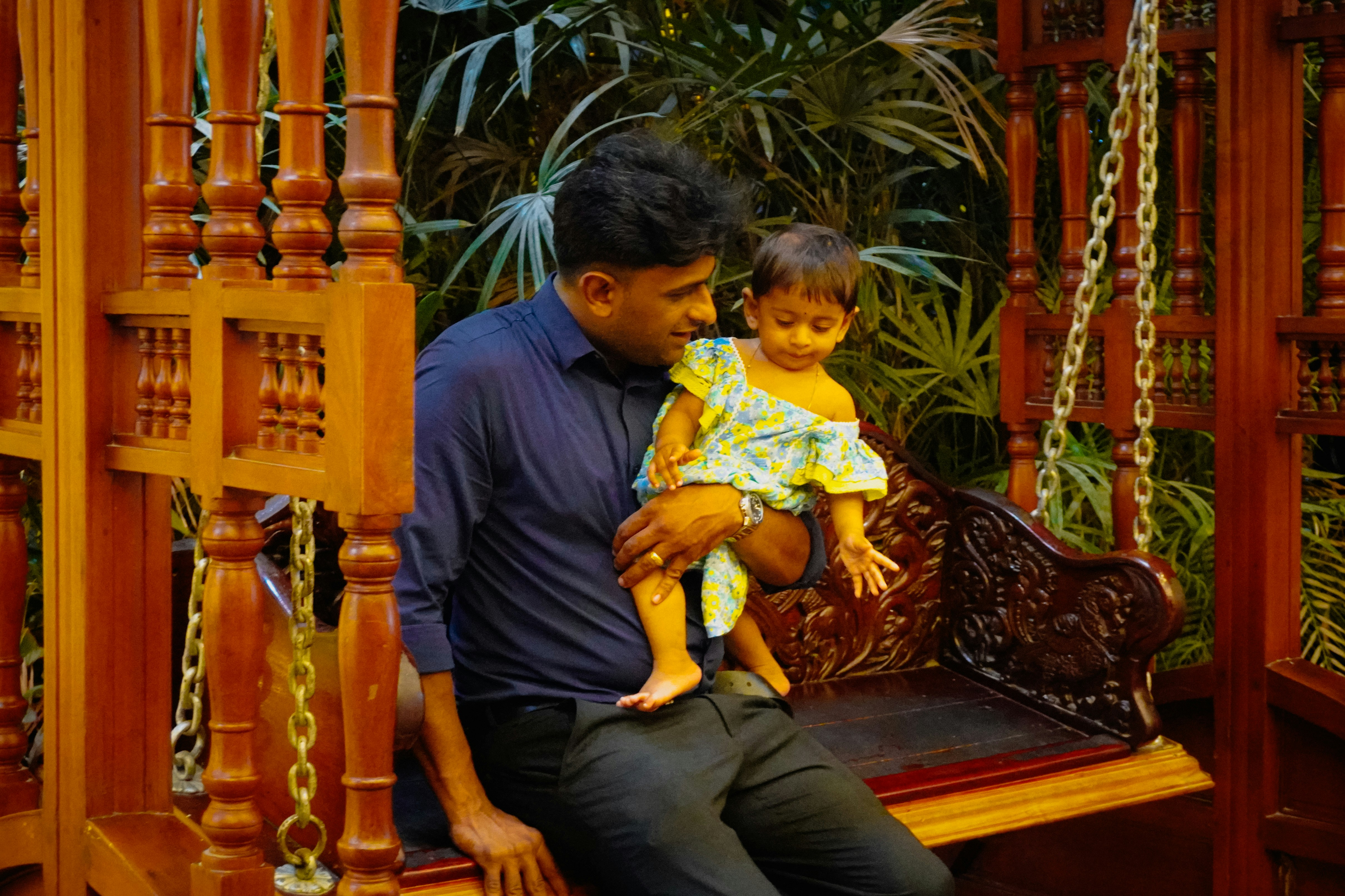 Father and Child on a Wooden Swing Amid Tropical Leaves