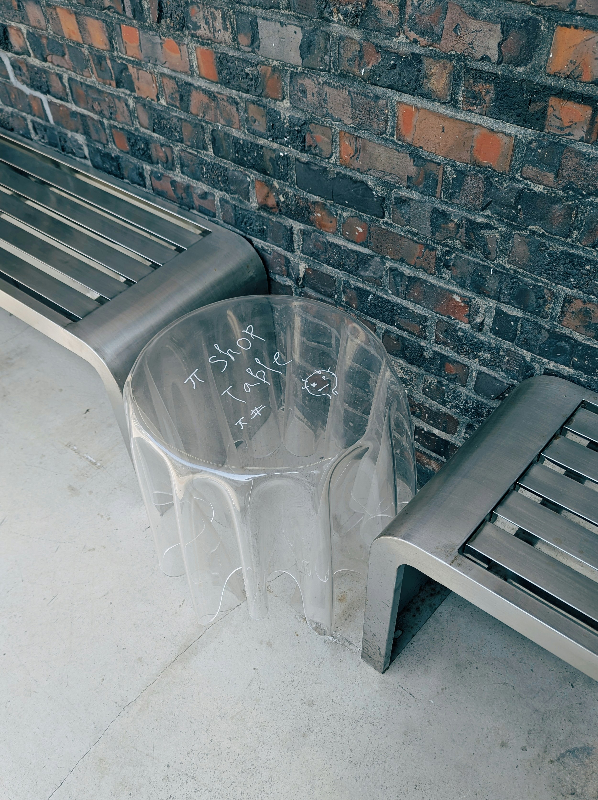 Clear Chair Graffiti Between Metal Benches Against Brick Wall