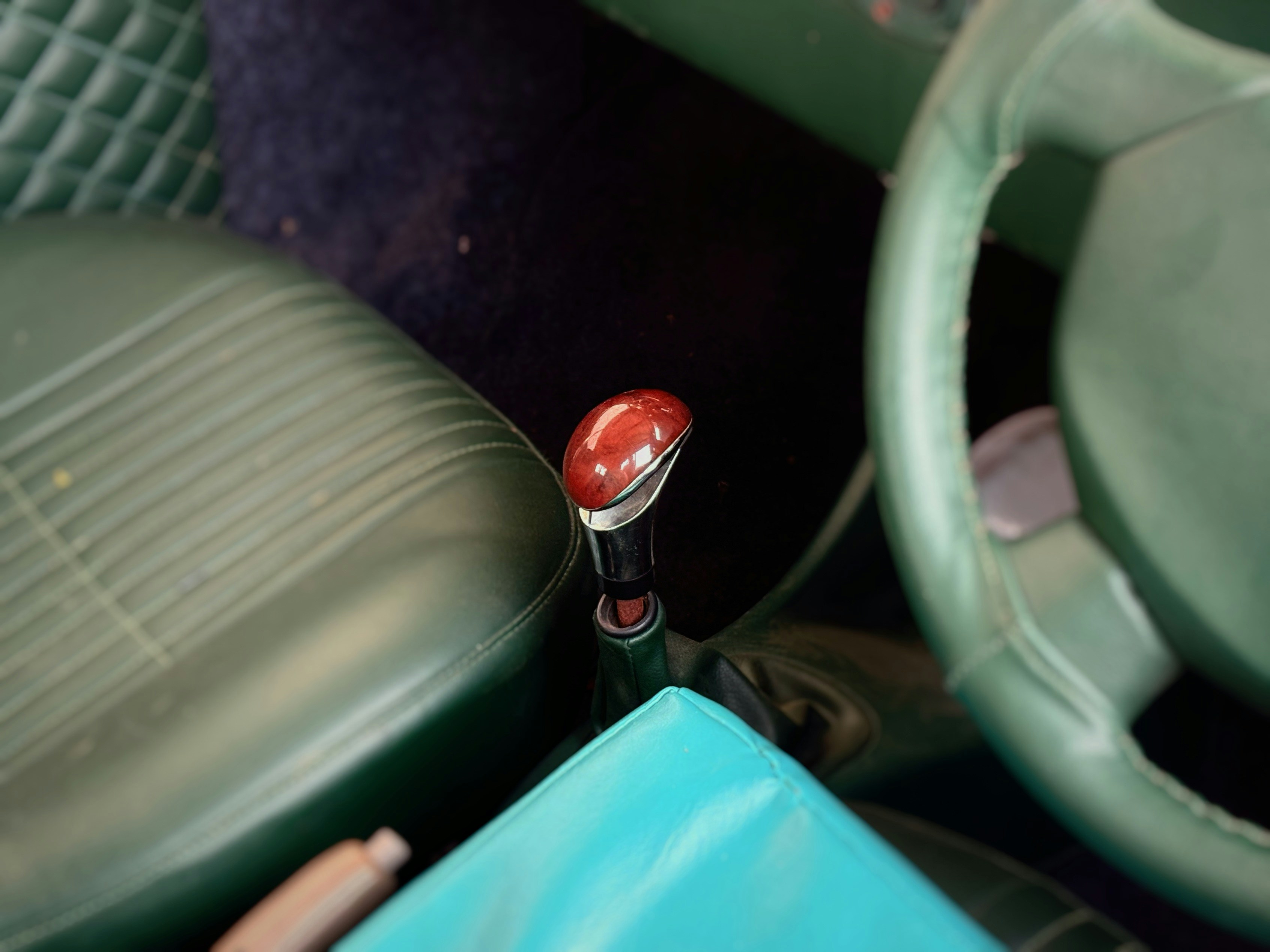 Polished mahogany gear knob and emerald green quilted leather interior of a vintage car, captured with a moody, film-inspired aesthetic emphasizing craftsmanship and classic automotive design.