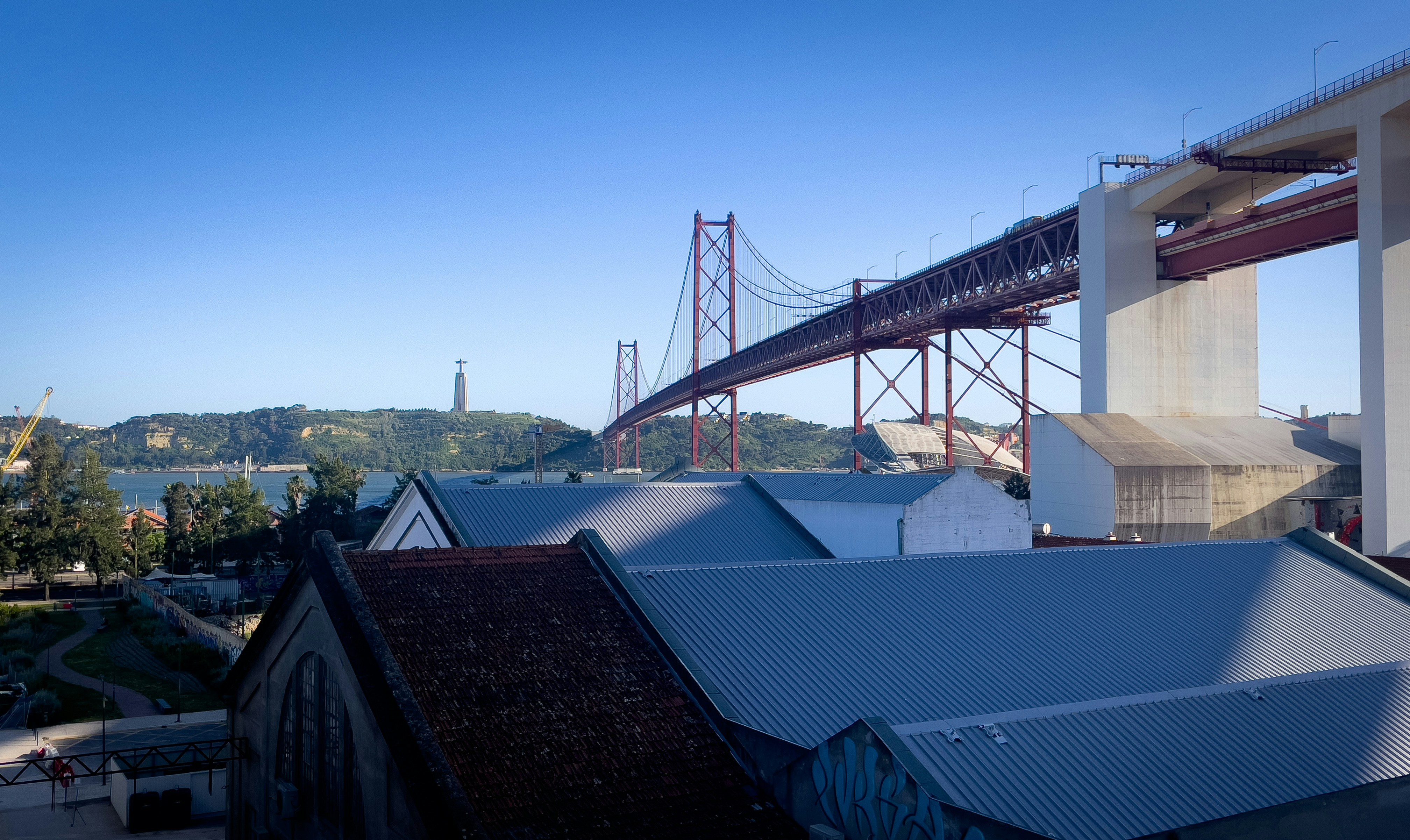 Blue Roofs Beneath a Red- painted Span: A Coastal City’s Bridge View