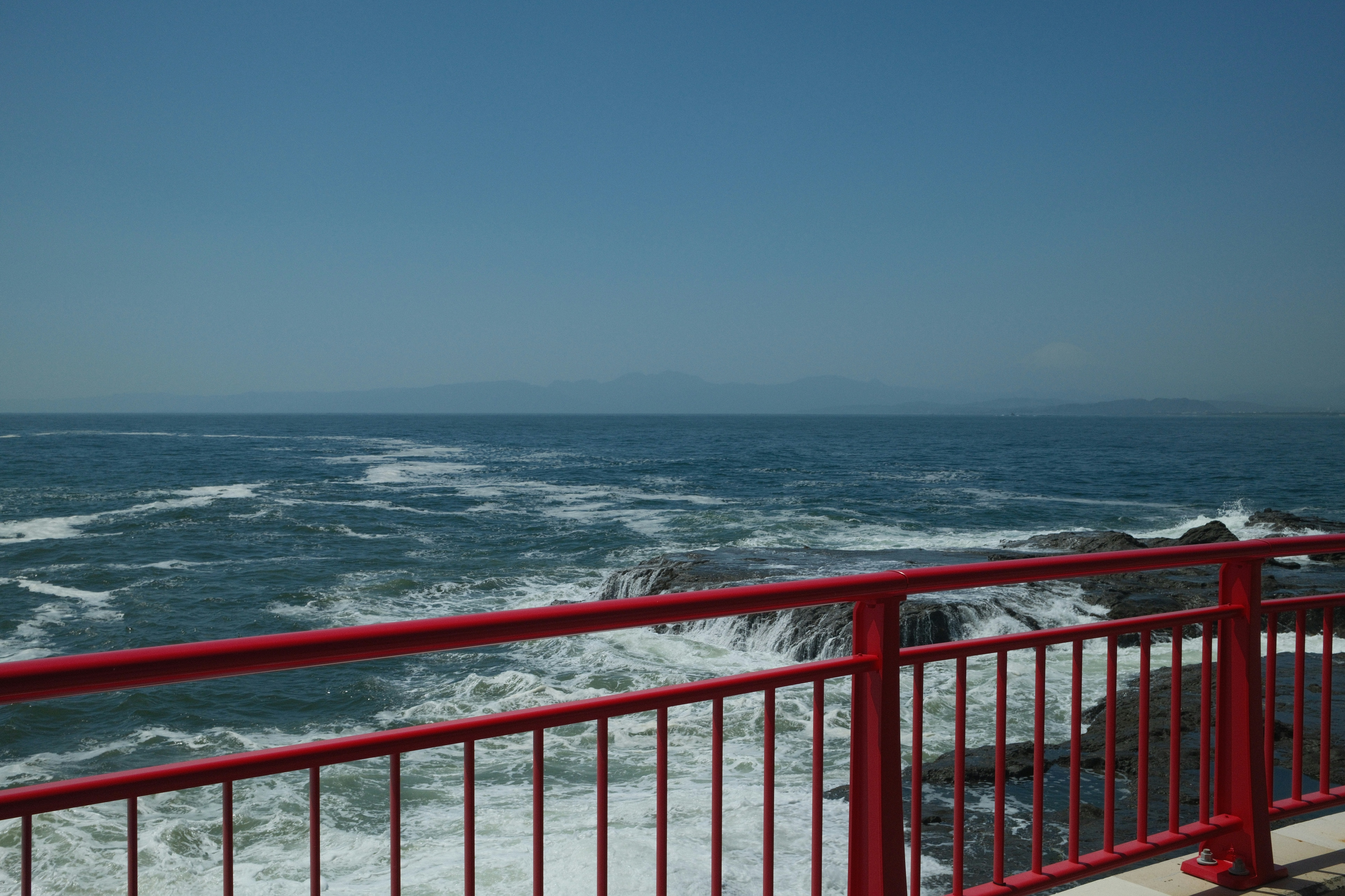 Red railing over the sea: a horizon of blue and spray
