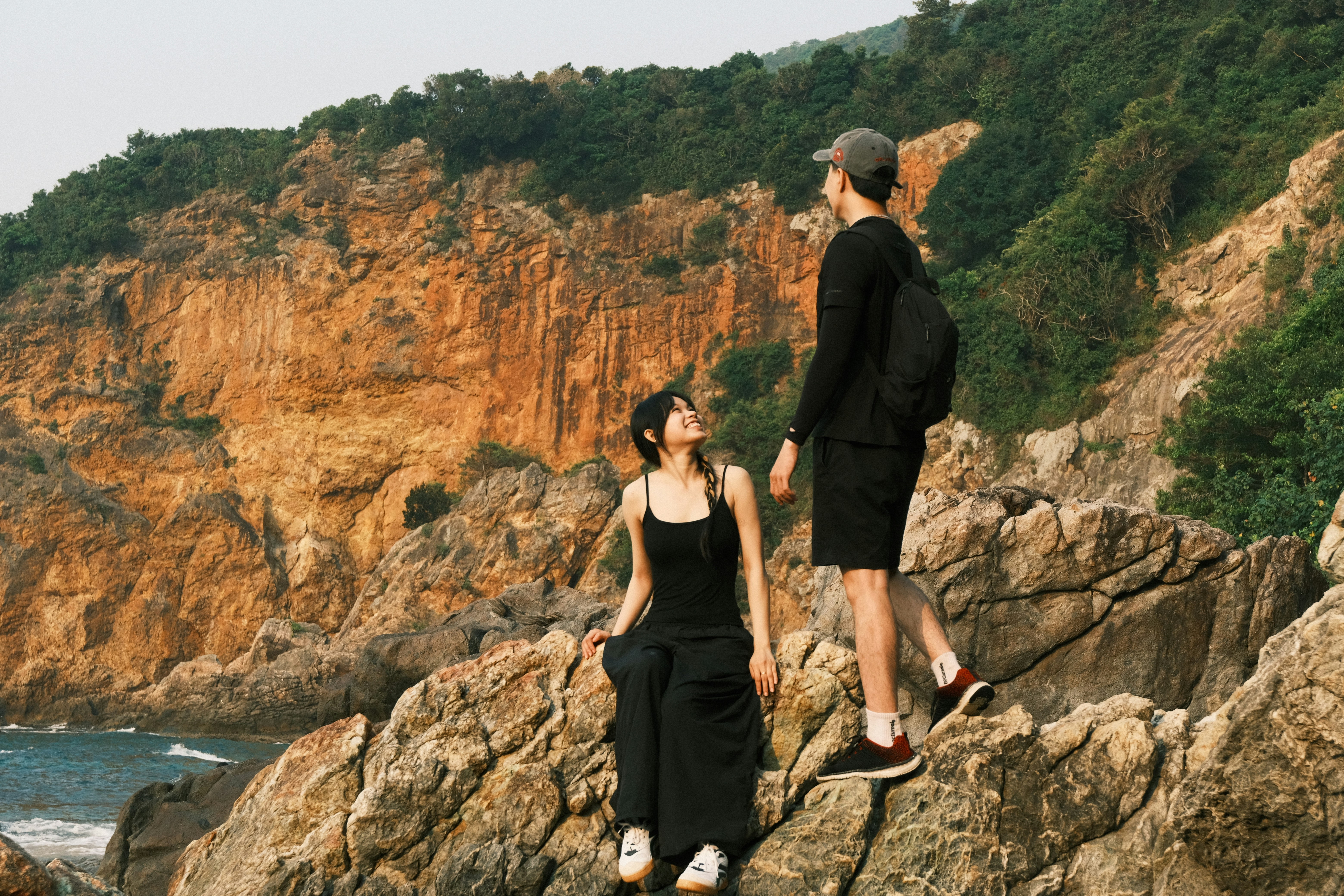 Two Travelers on Coastal Cliffs: Quiet Moment Amid Orange Rock and Sea