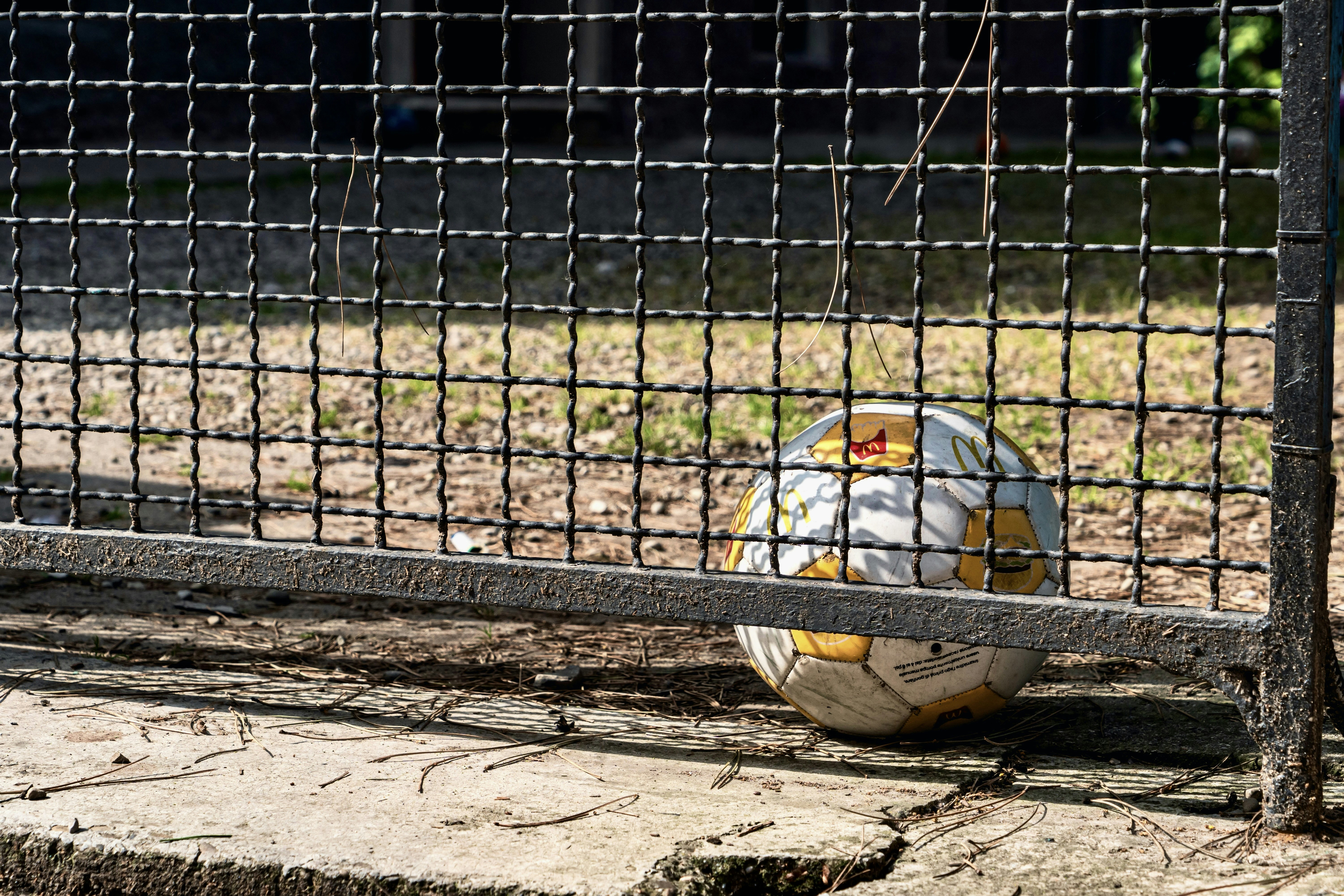 Ball Resting Behind a Weathered Gate on a Sunlit Pitch
