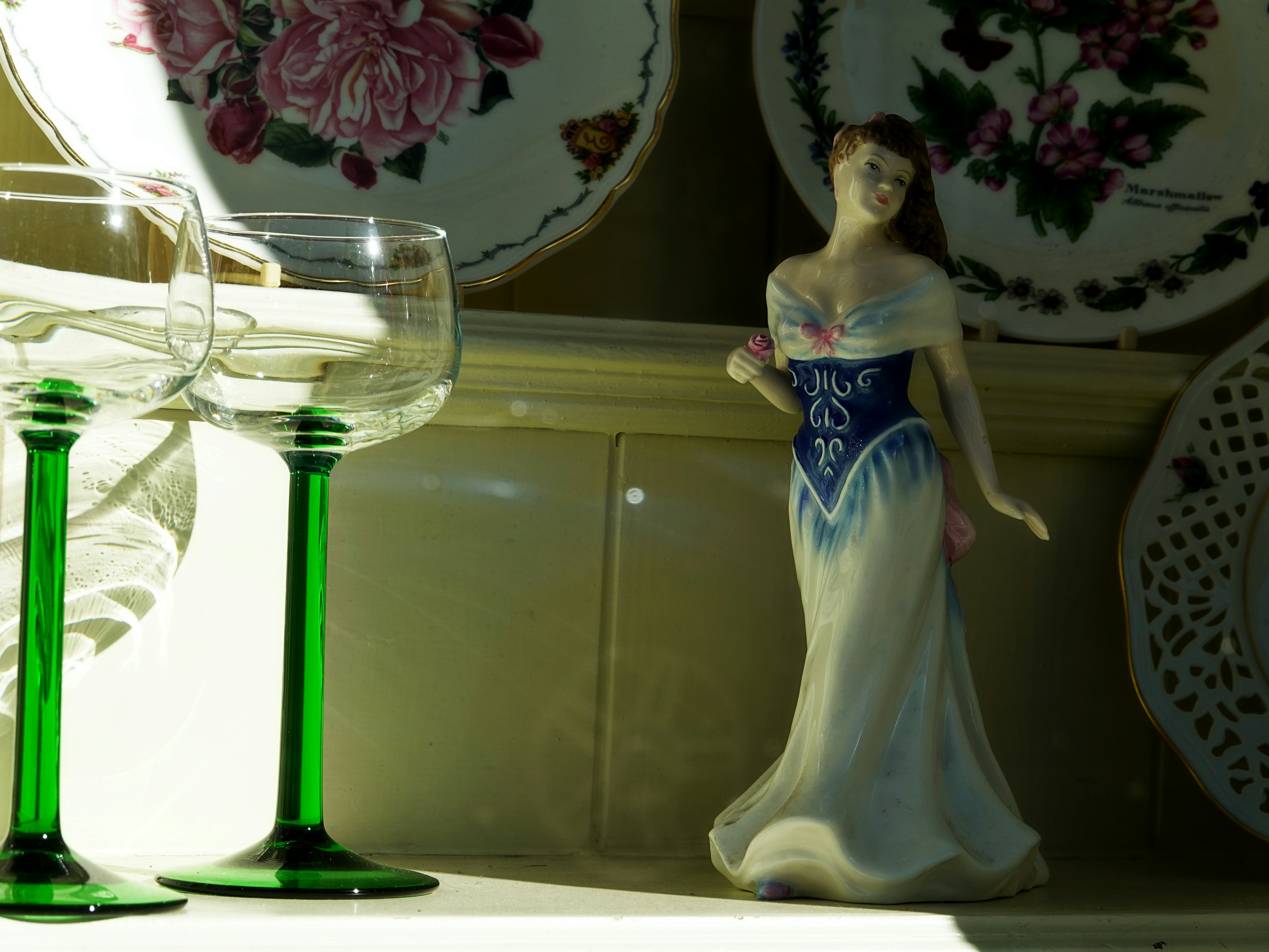 Ceramic Elegance: A porcelain figurine amid glassware on a illuminated shelf