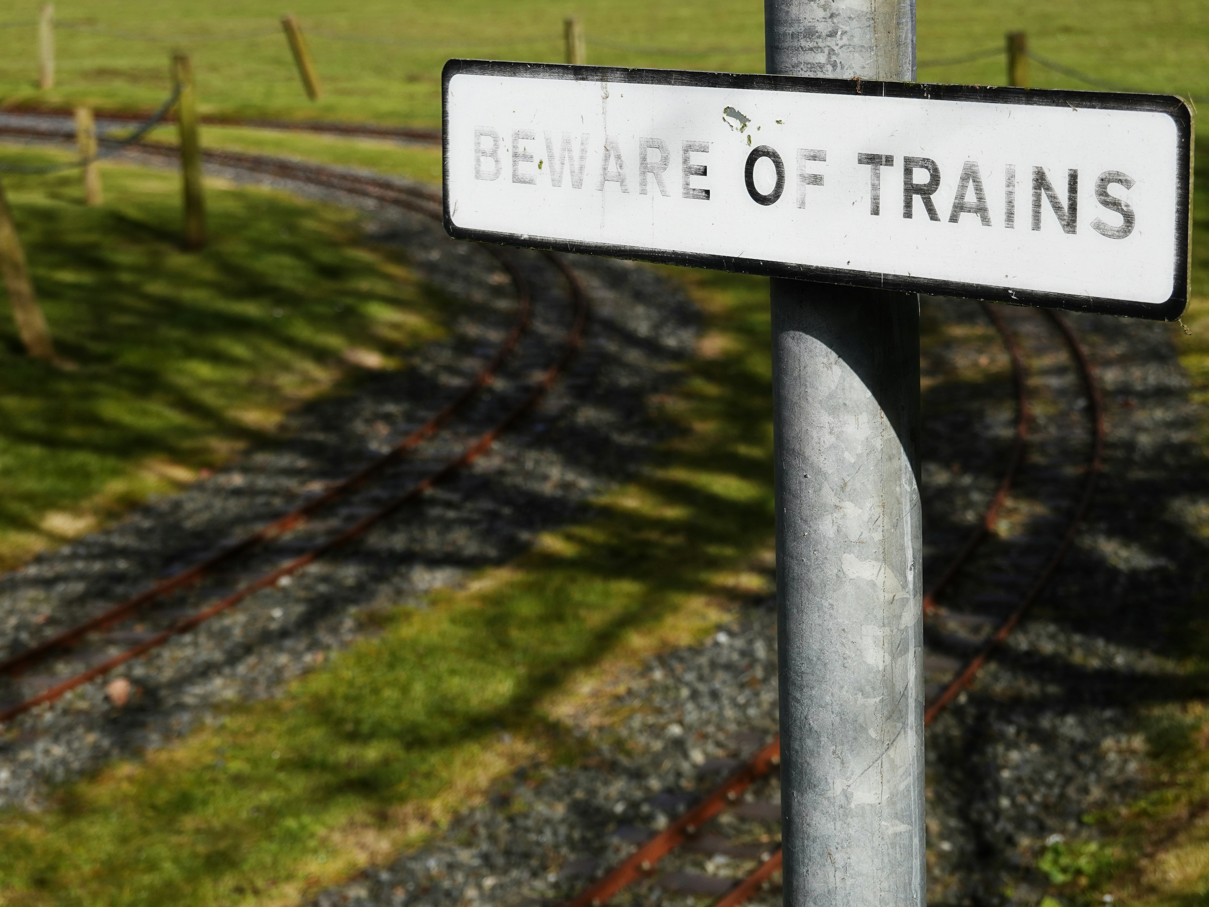 Beware of Trains: A Rusted Sign by Curving Rails