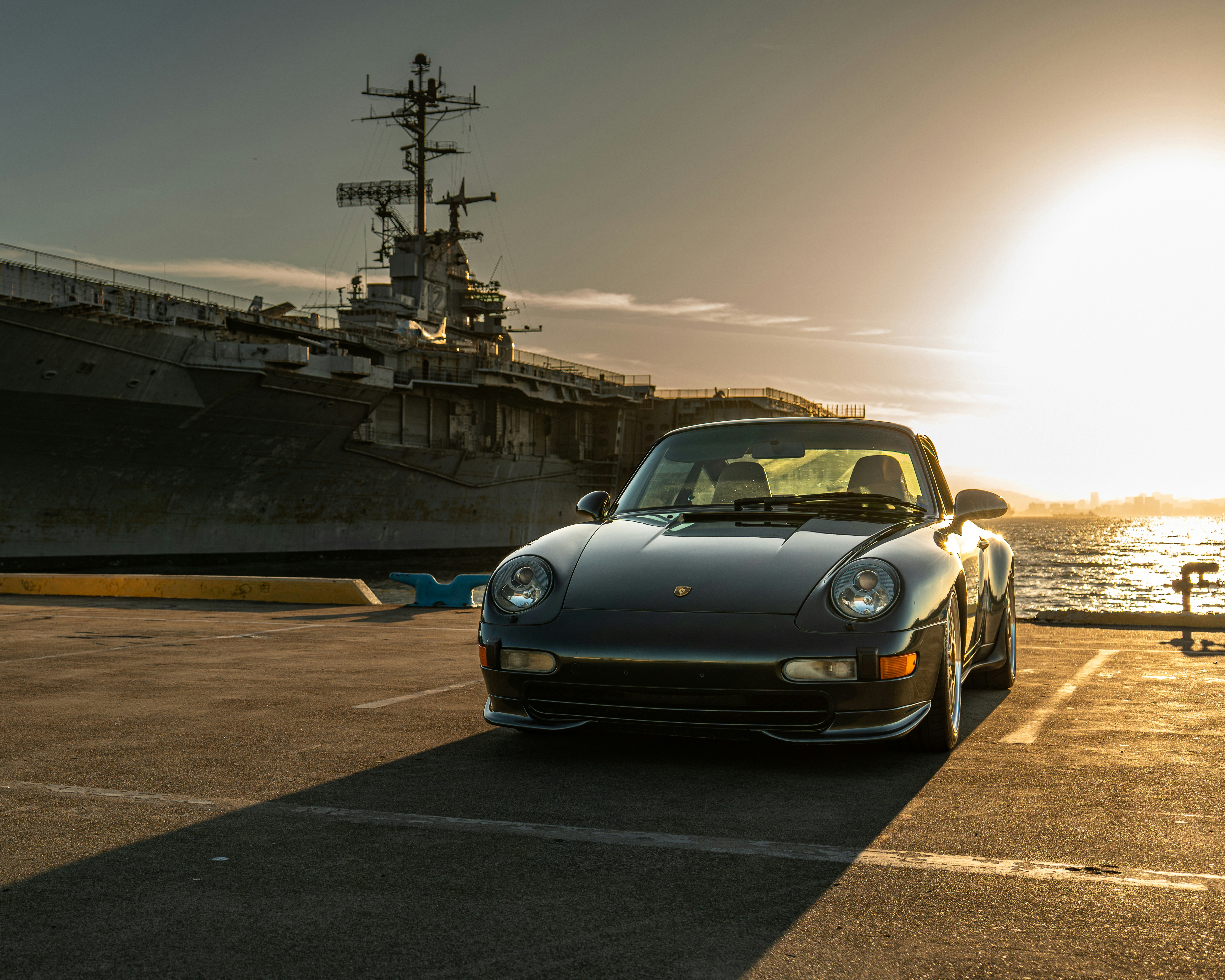 Sunlit Porsche on the Deck With a Warship Backdrop at Dusk