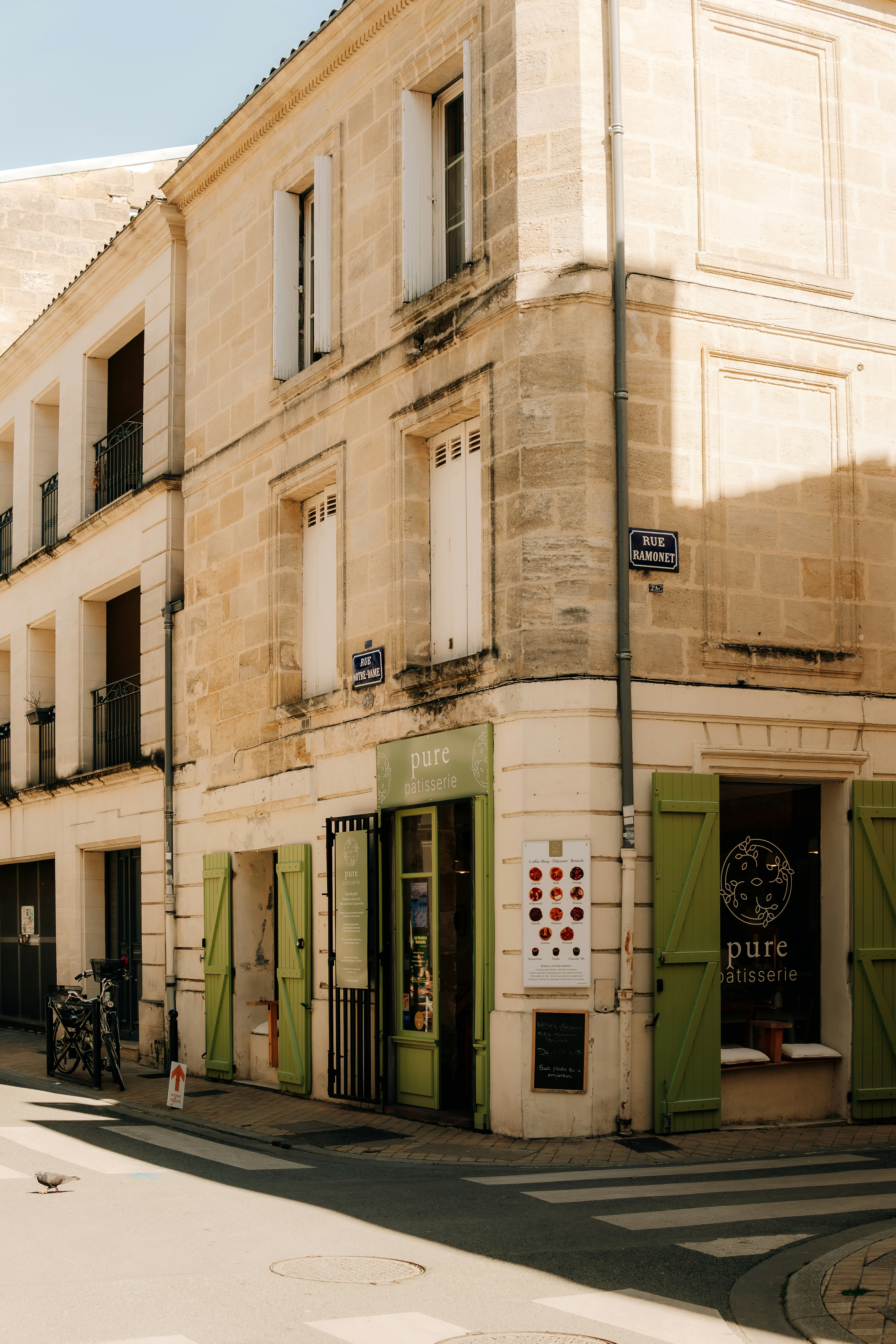 Sunlit cream facade and green shutters at a quiet street corner