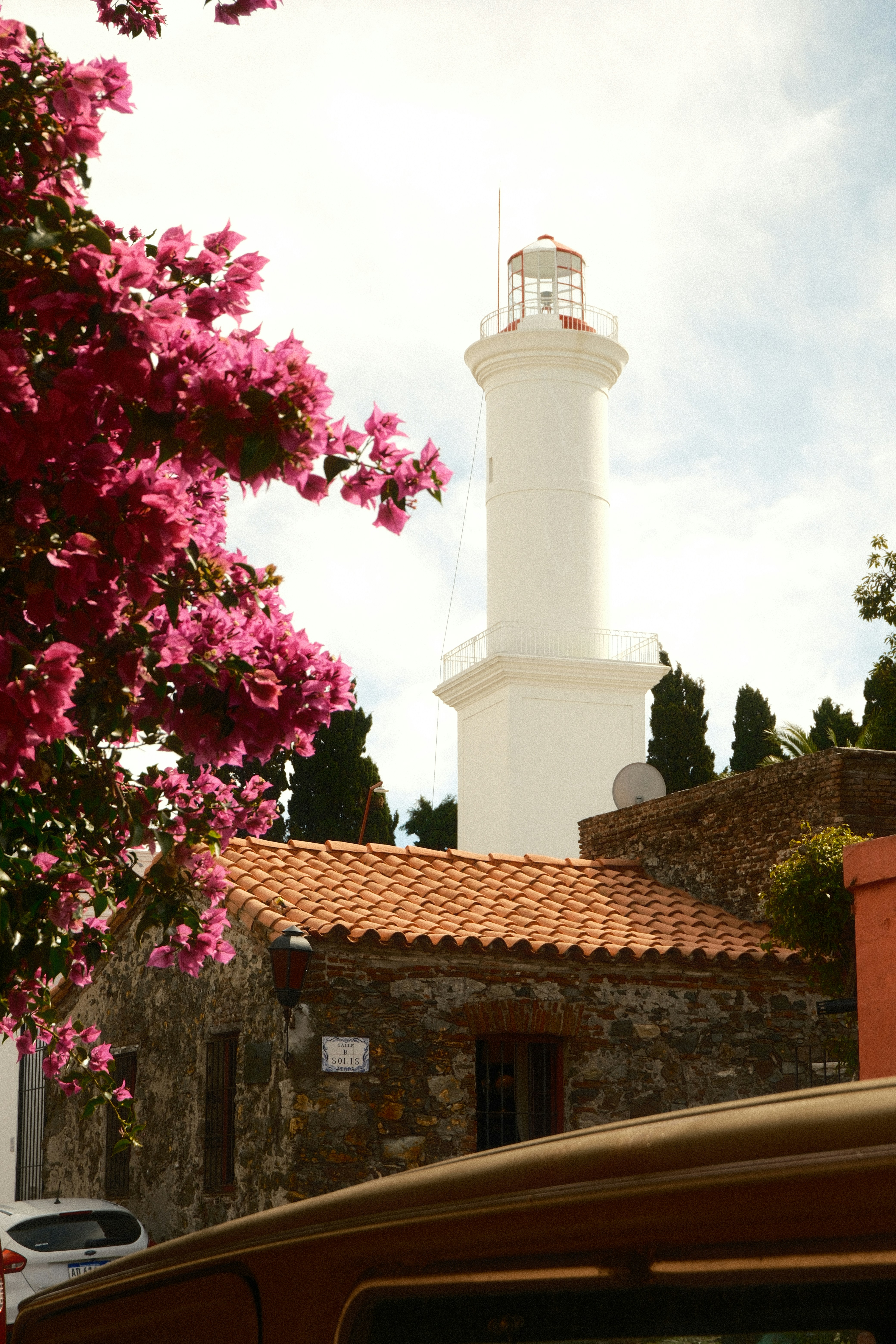 White Lighthouse Amid Pink Bougainvillea and Old Stone House
