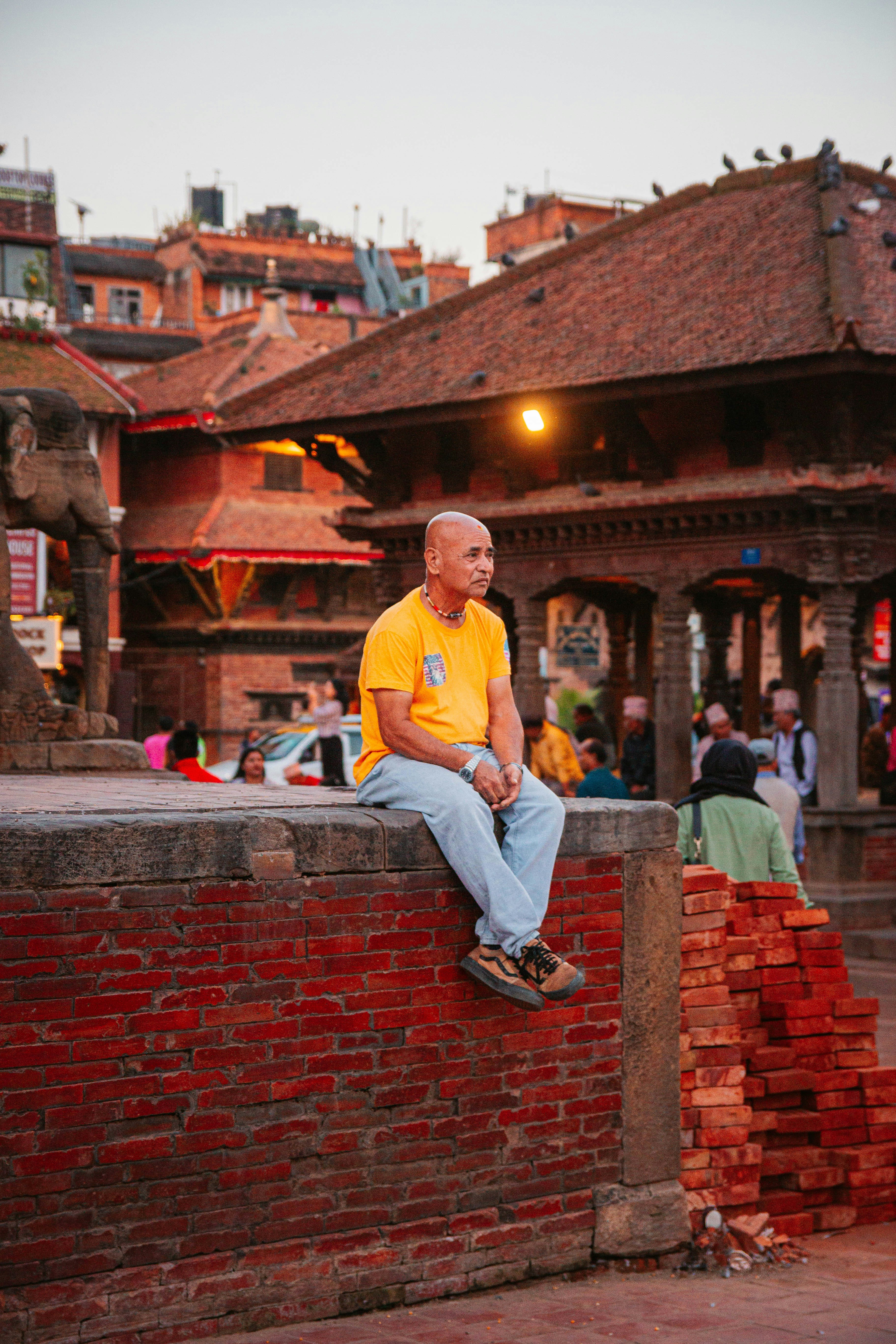 Yellow-shirted on the brick ledge: a moment of stillness in a bustling Nepali square