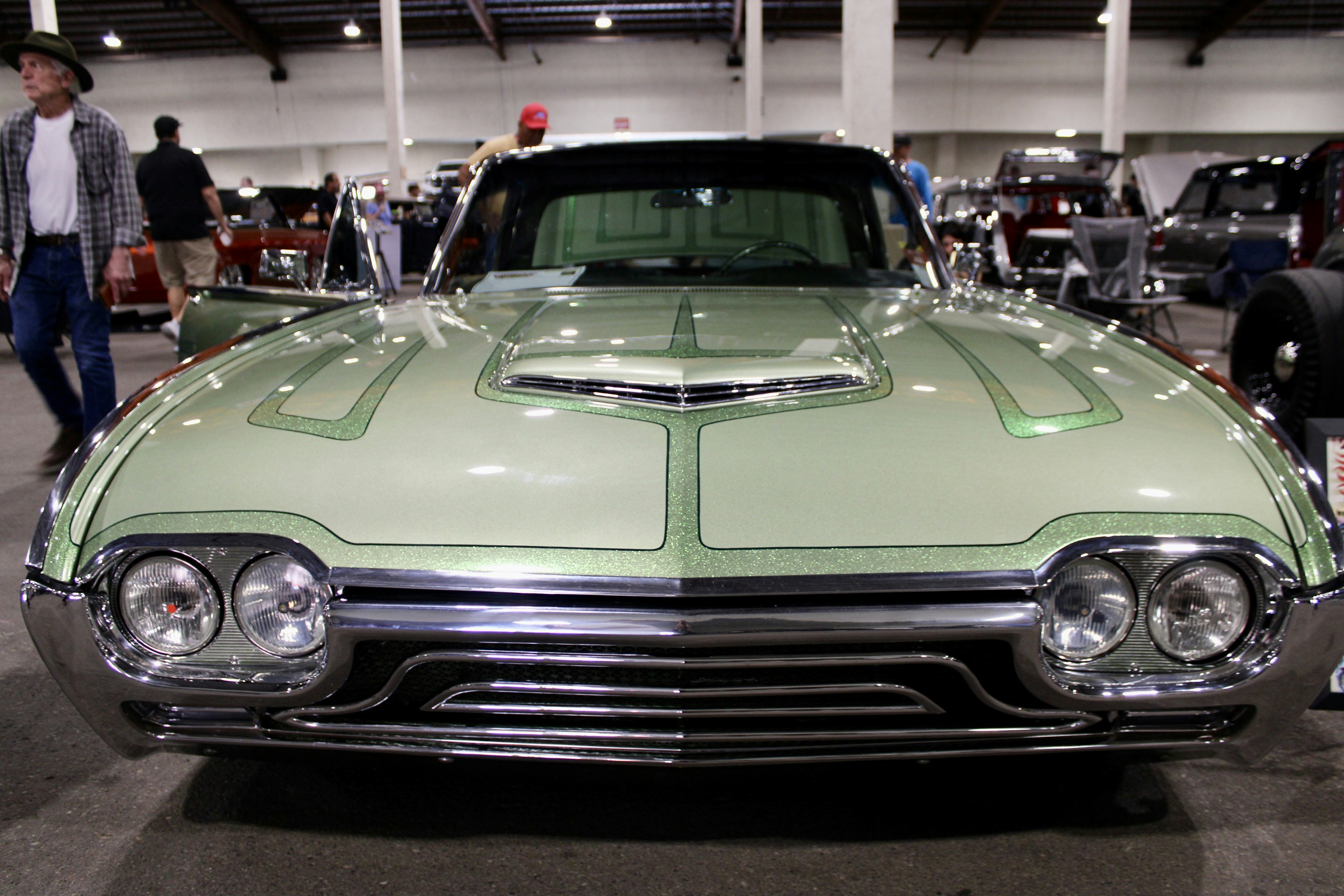 Mint-green Classic: Chrome Grille and Hood Details at an Indoor Car Show