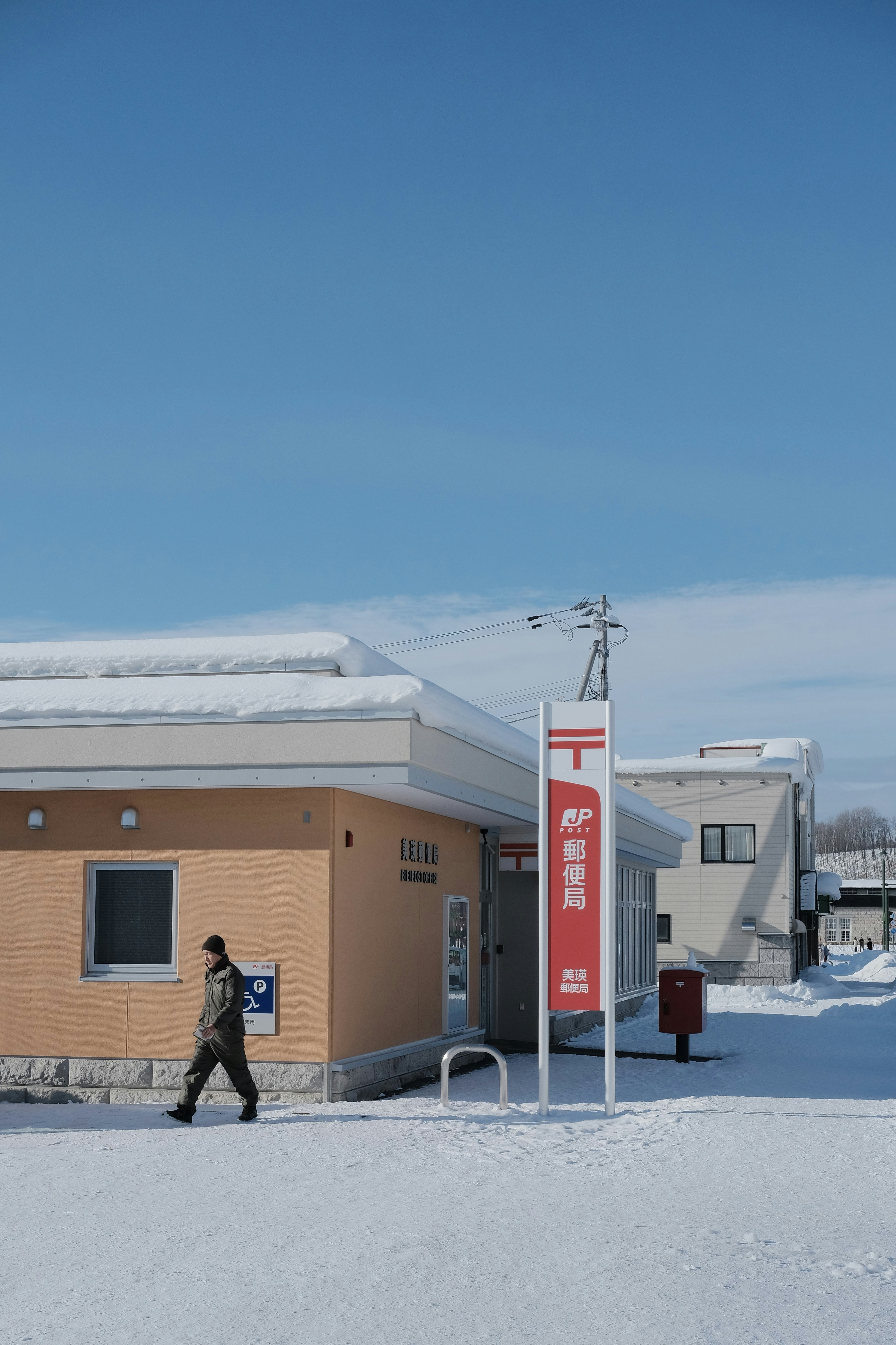 Snowcoat Street: A solitary commuter beside a sunlit post office