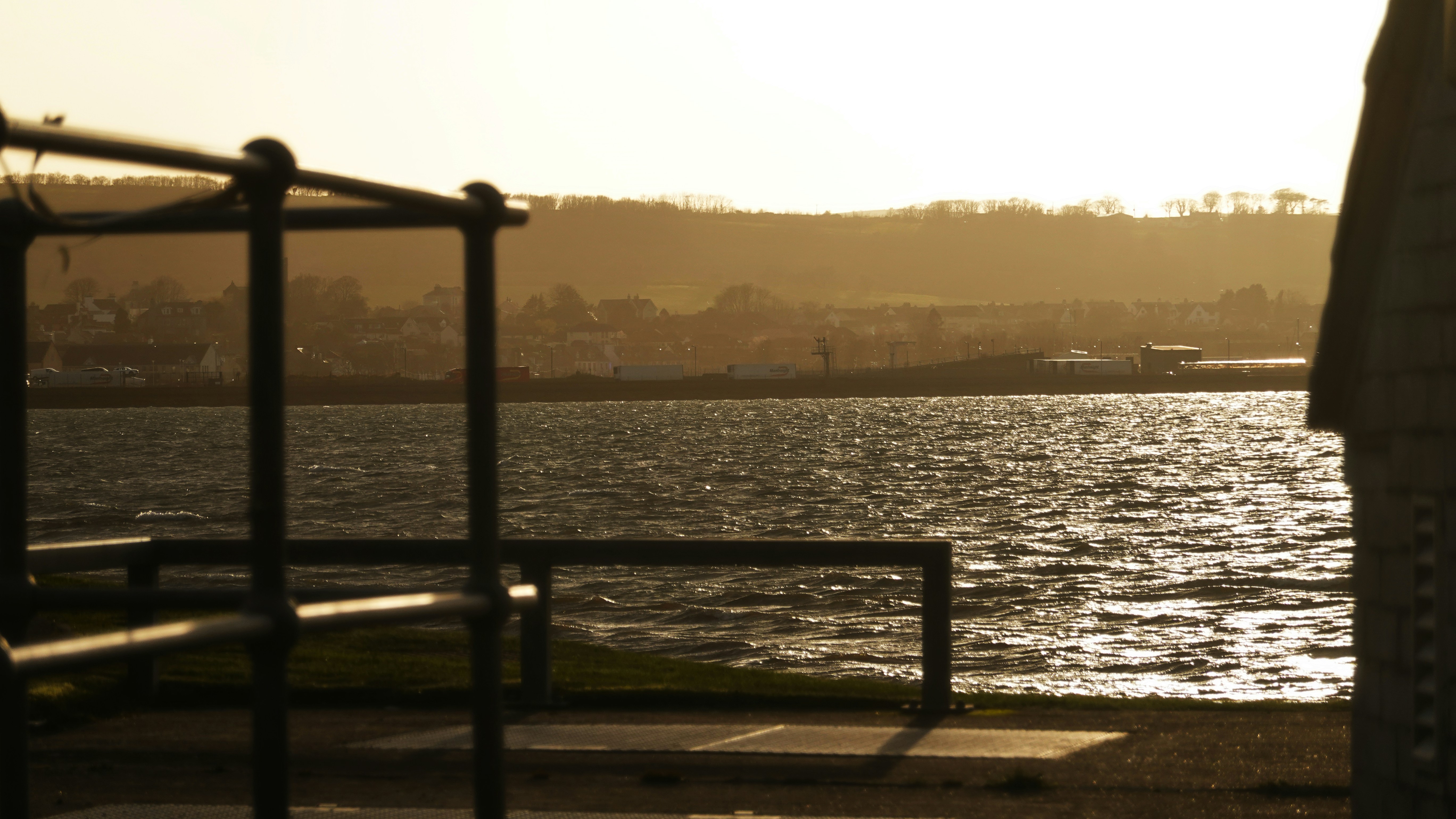 Sunlit quay: railing silhouettes and shimmering water at dusk