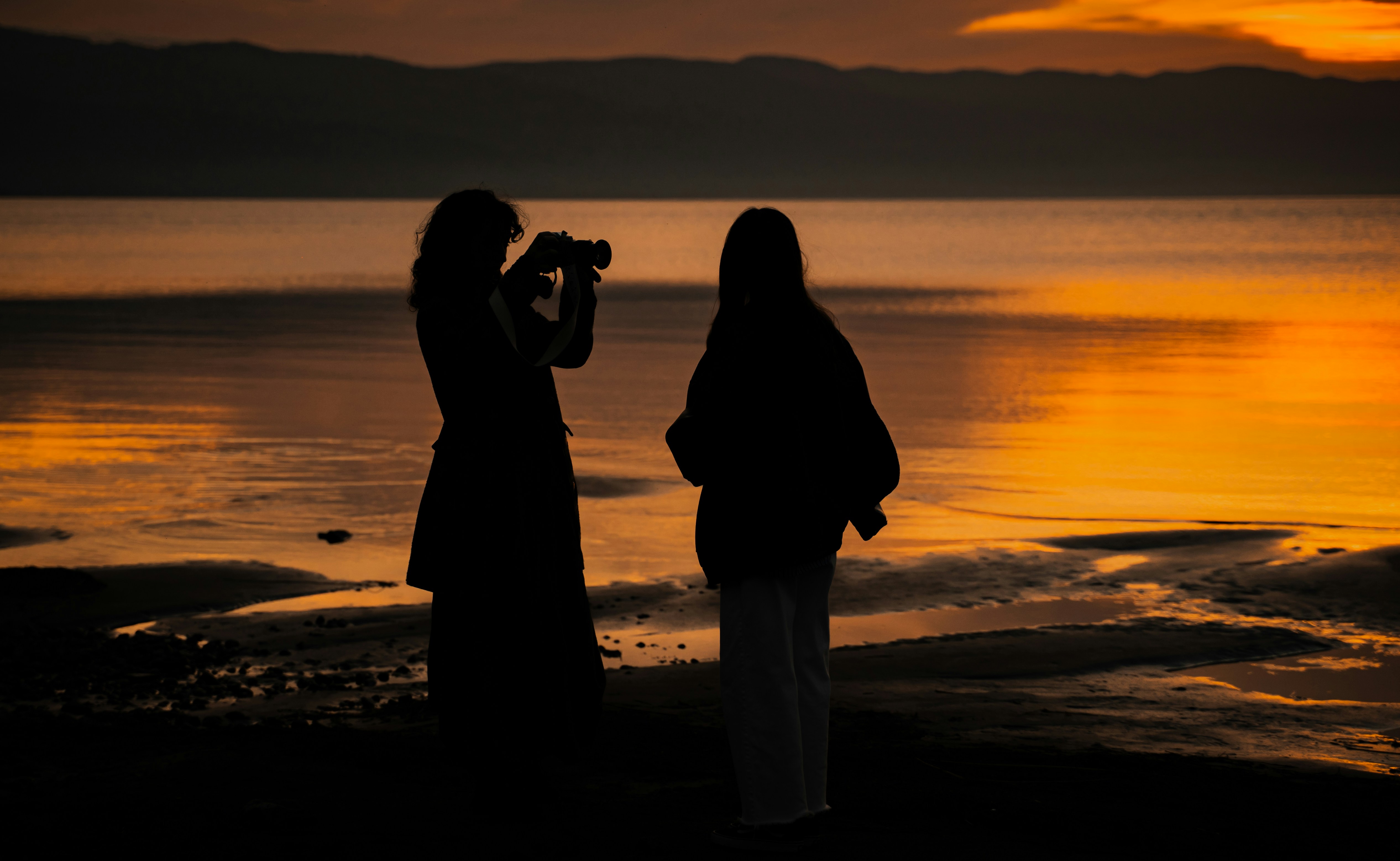 Two Silhouettes at Dusk: A Photographer and a Companion by the Shore