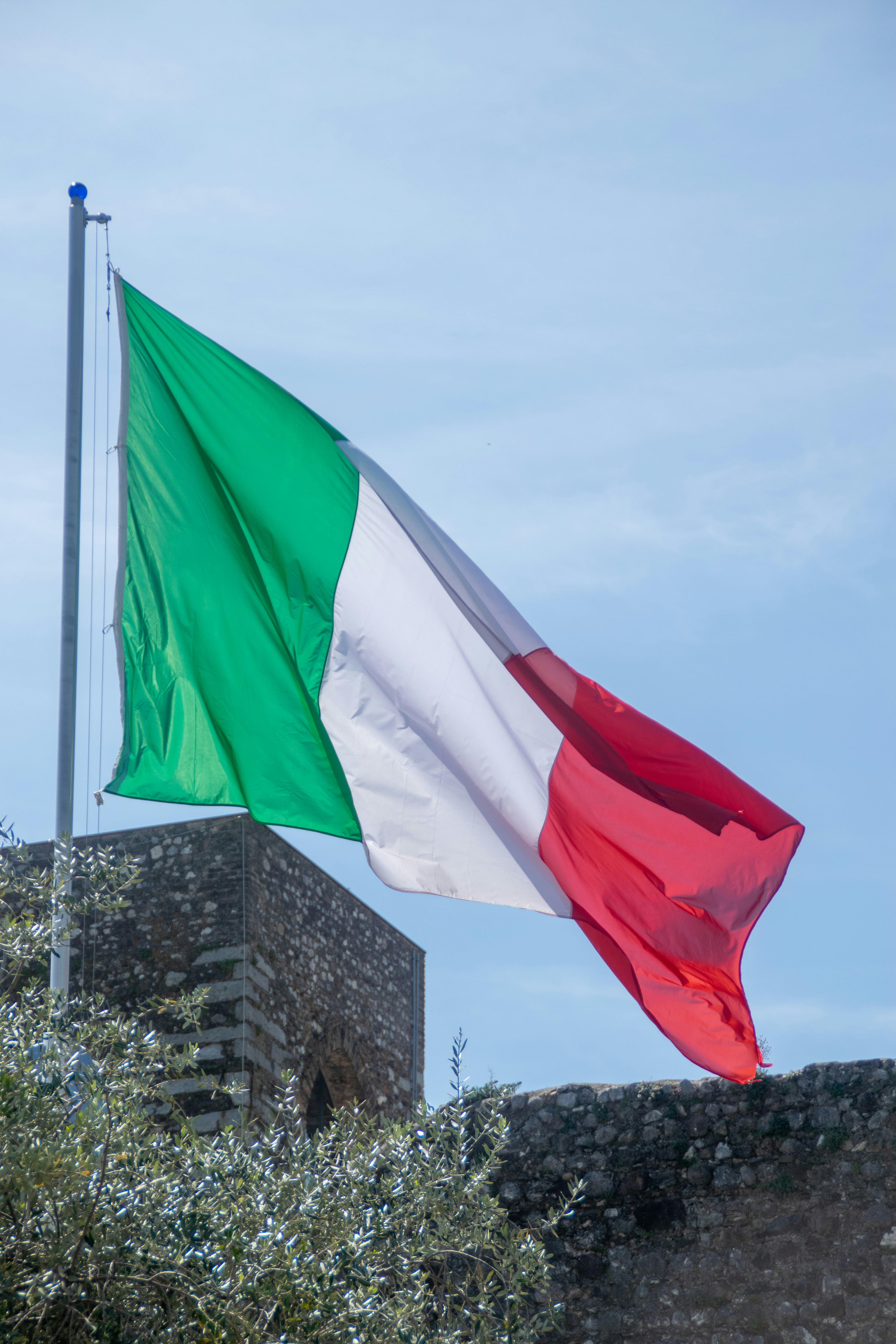 Flag of Italy unfurling above ancient stone walls
