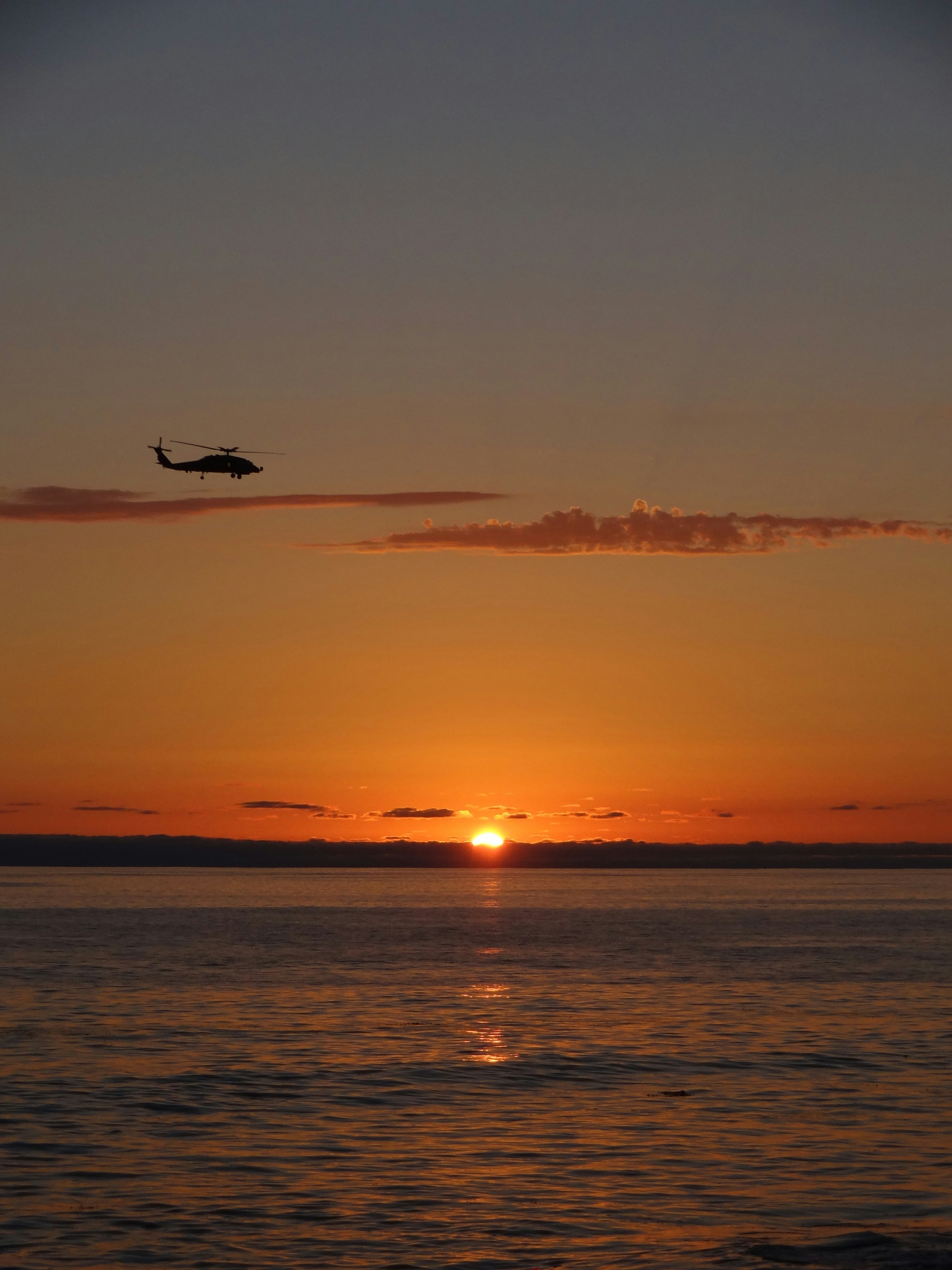 Sunset Over Calm Waters: A Helicopter Silhouette in Silence