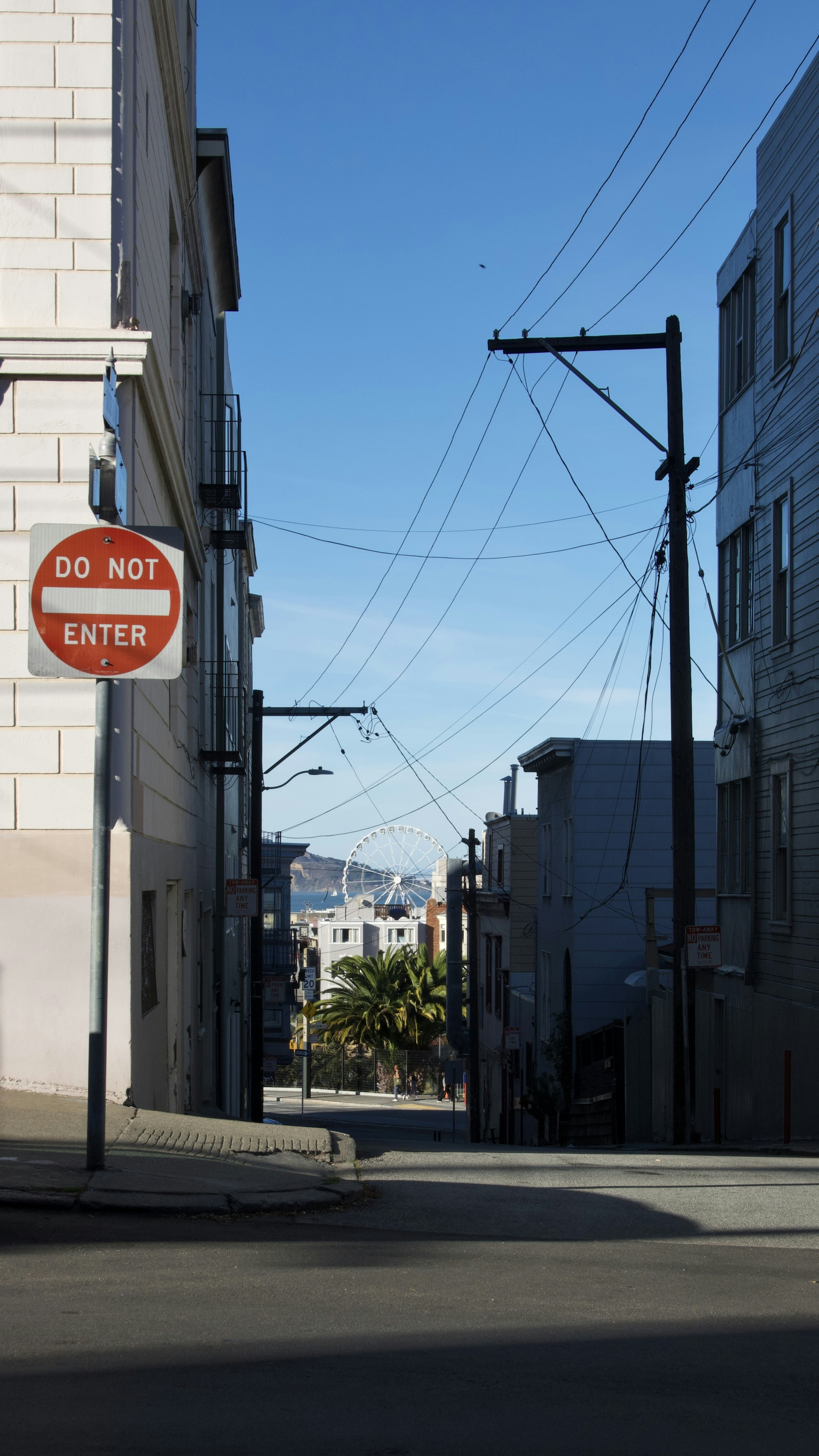 Narrow Street to the Ocean Arc: A Distant Ferris Wheel Framed by Urban Shadows