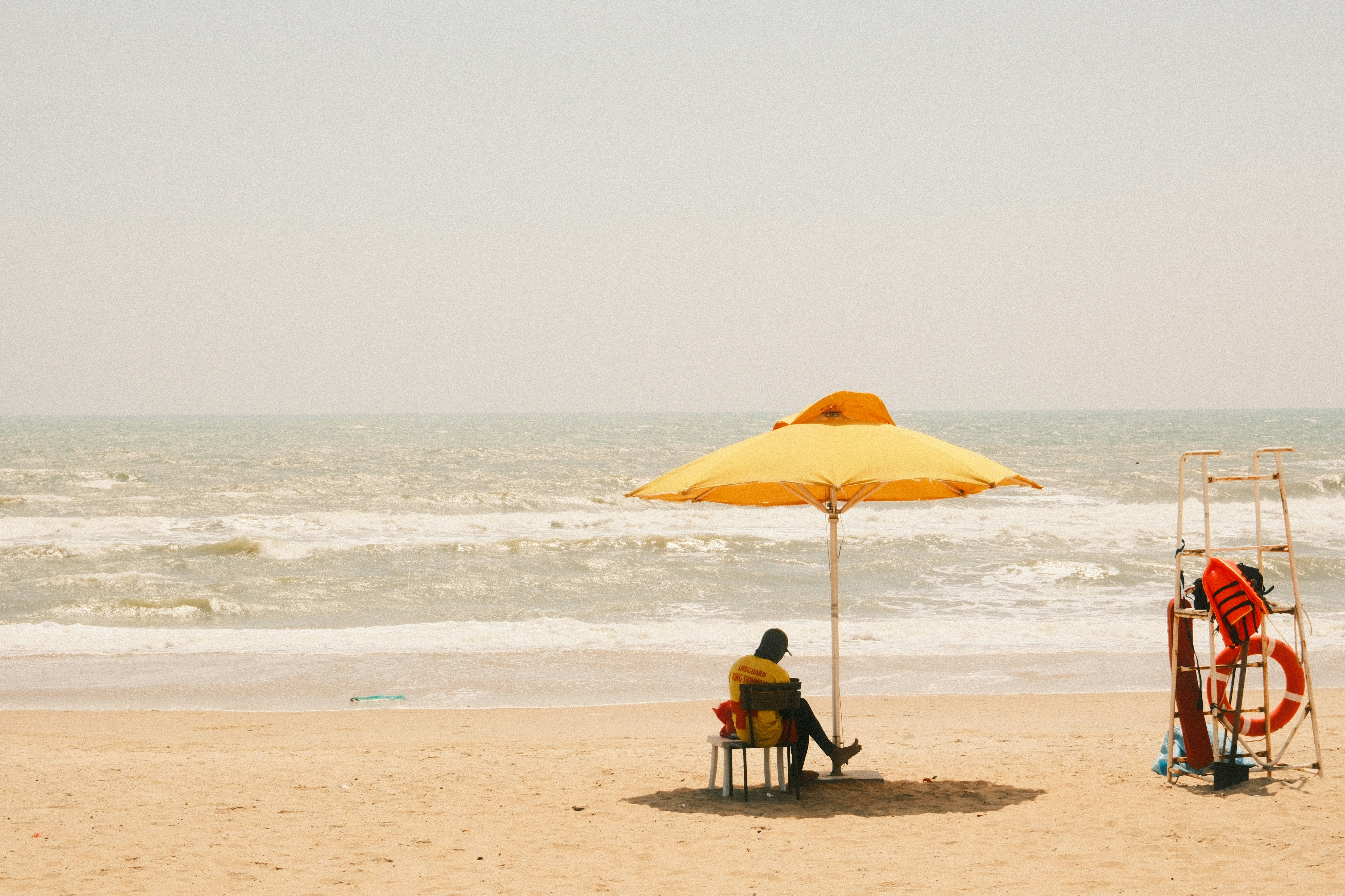 Seaside Vigil: A Lone Seater Under a Sunny Umbrella