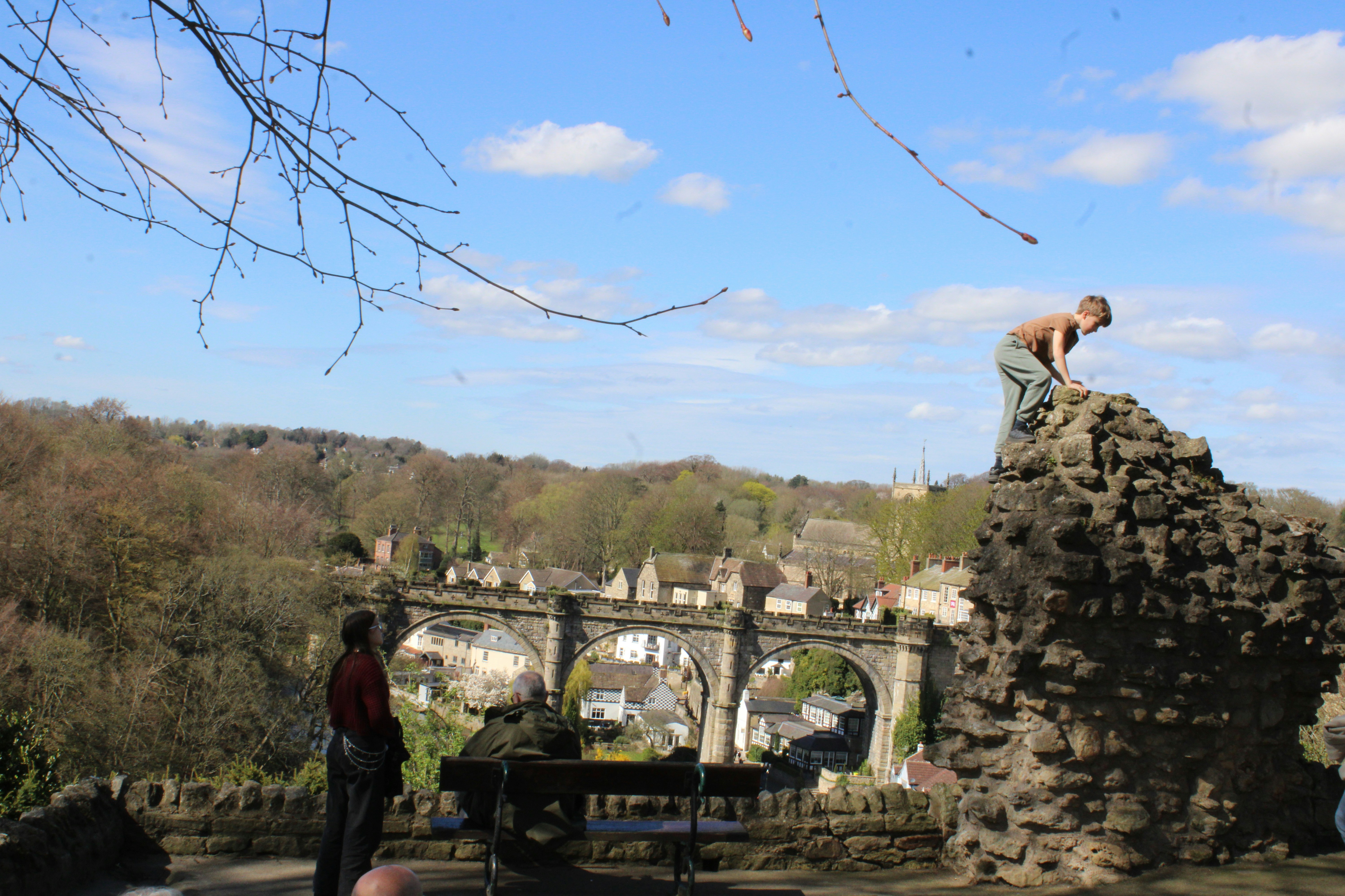 Stout climber atop ancient ruins with village bridge in the background