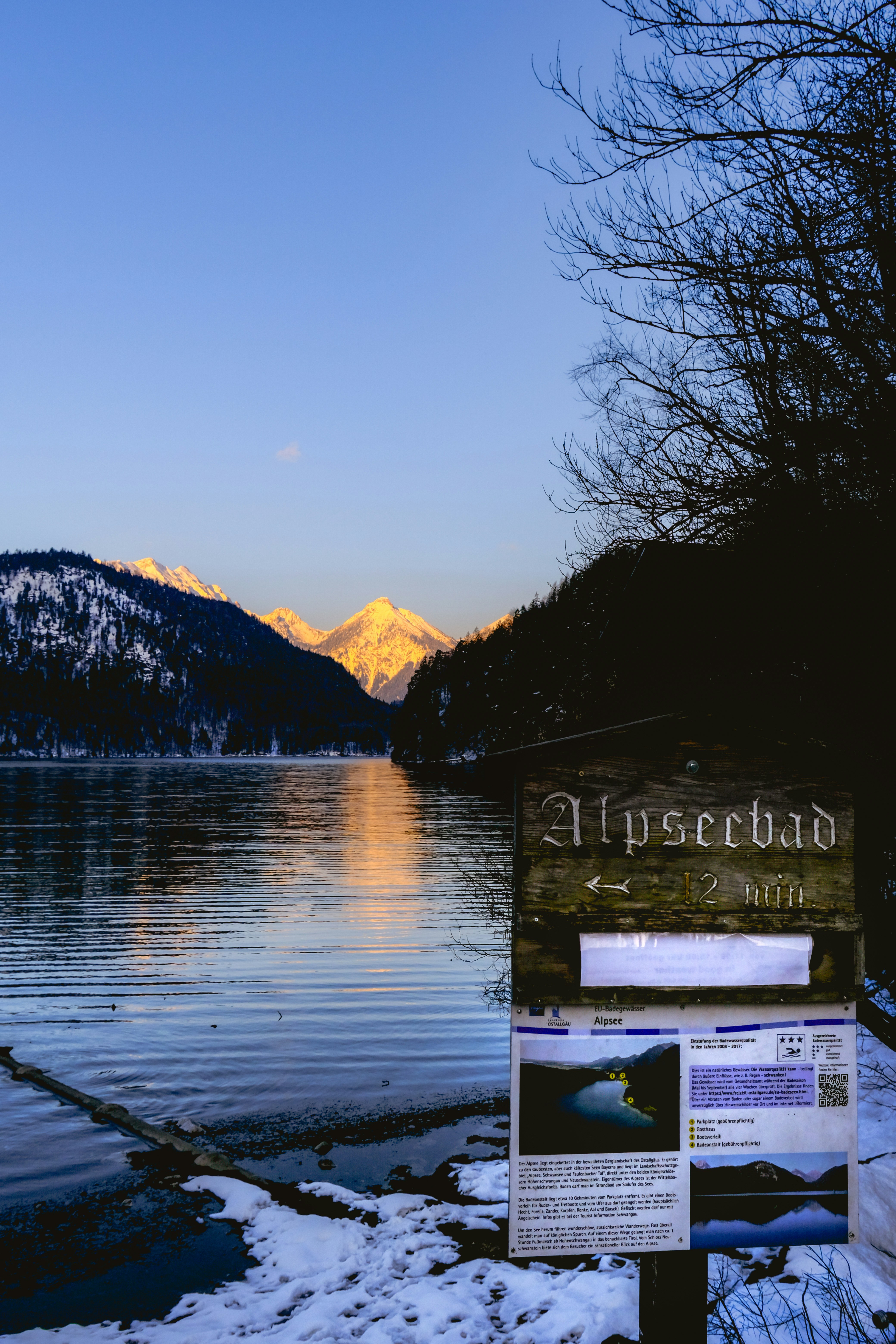 Sunlit Alps Reflect in Frozen Lake at Alpine Signpost