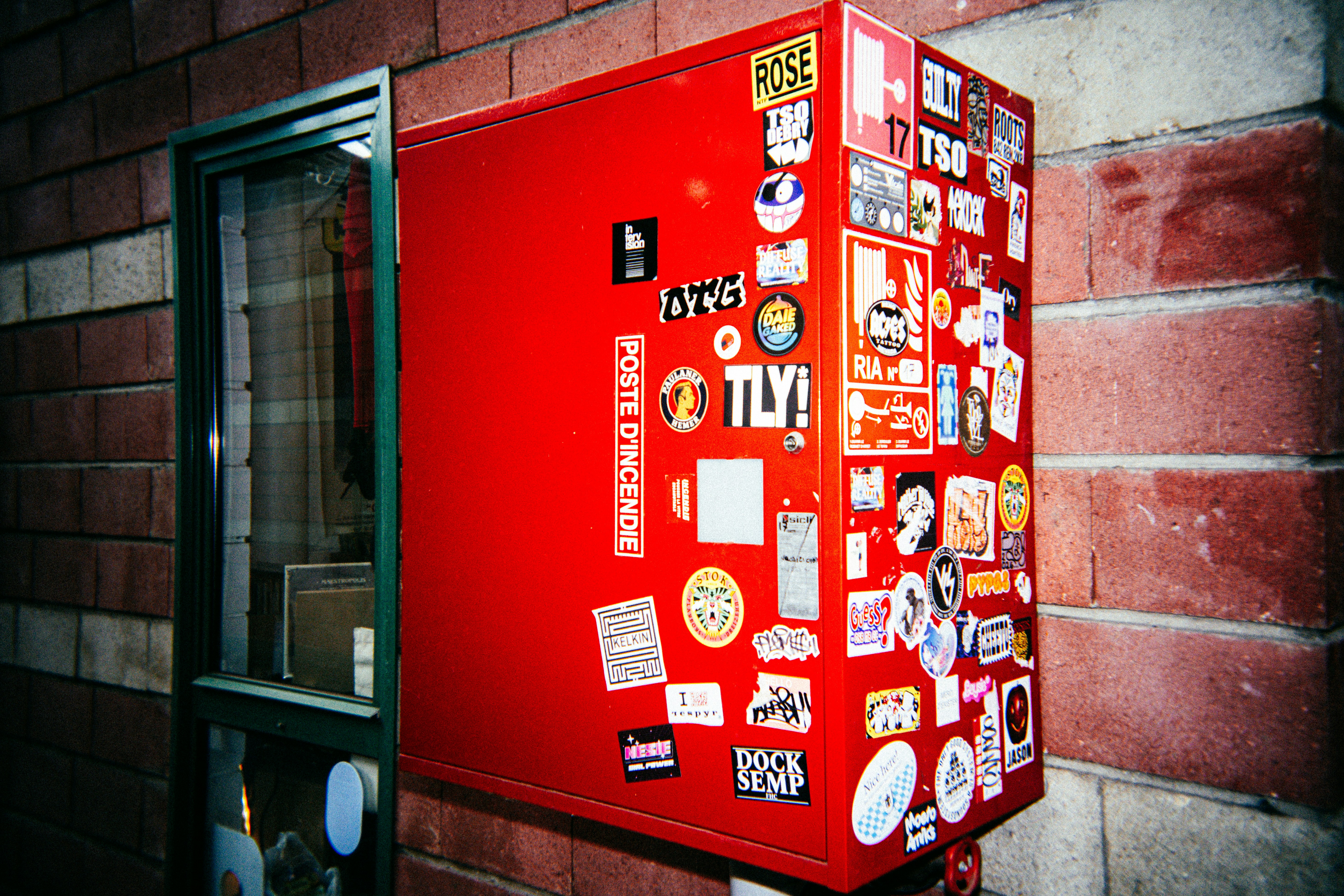 Stickered Red Mailbox on a Brick Wall Corner