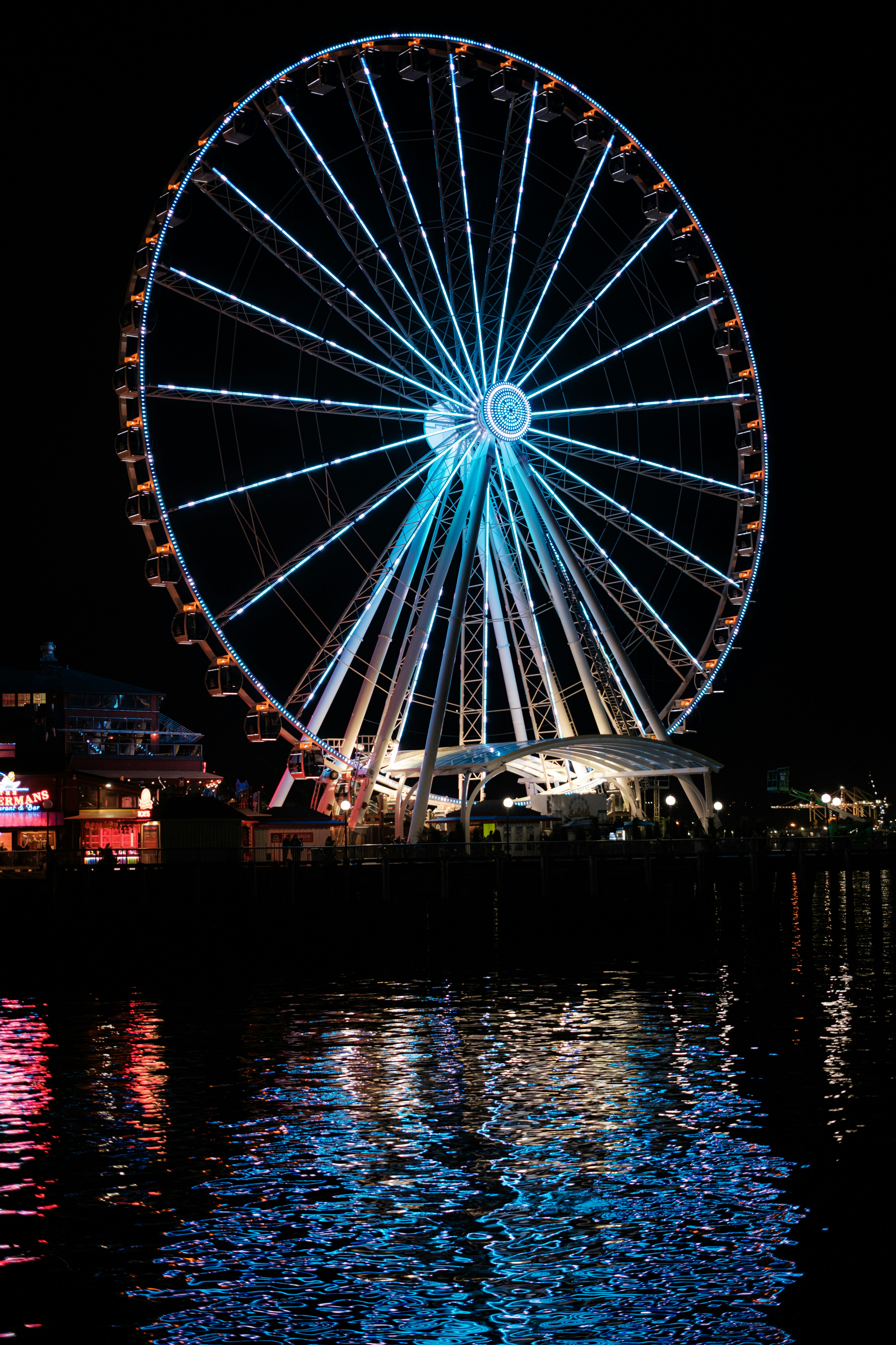 Neon Wheel of Night: Illuminated Ferris Wheel over Calm Pier