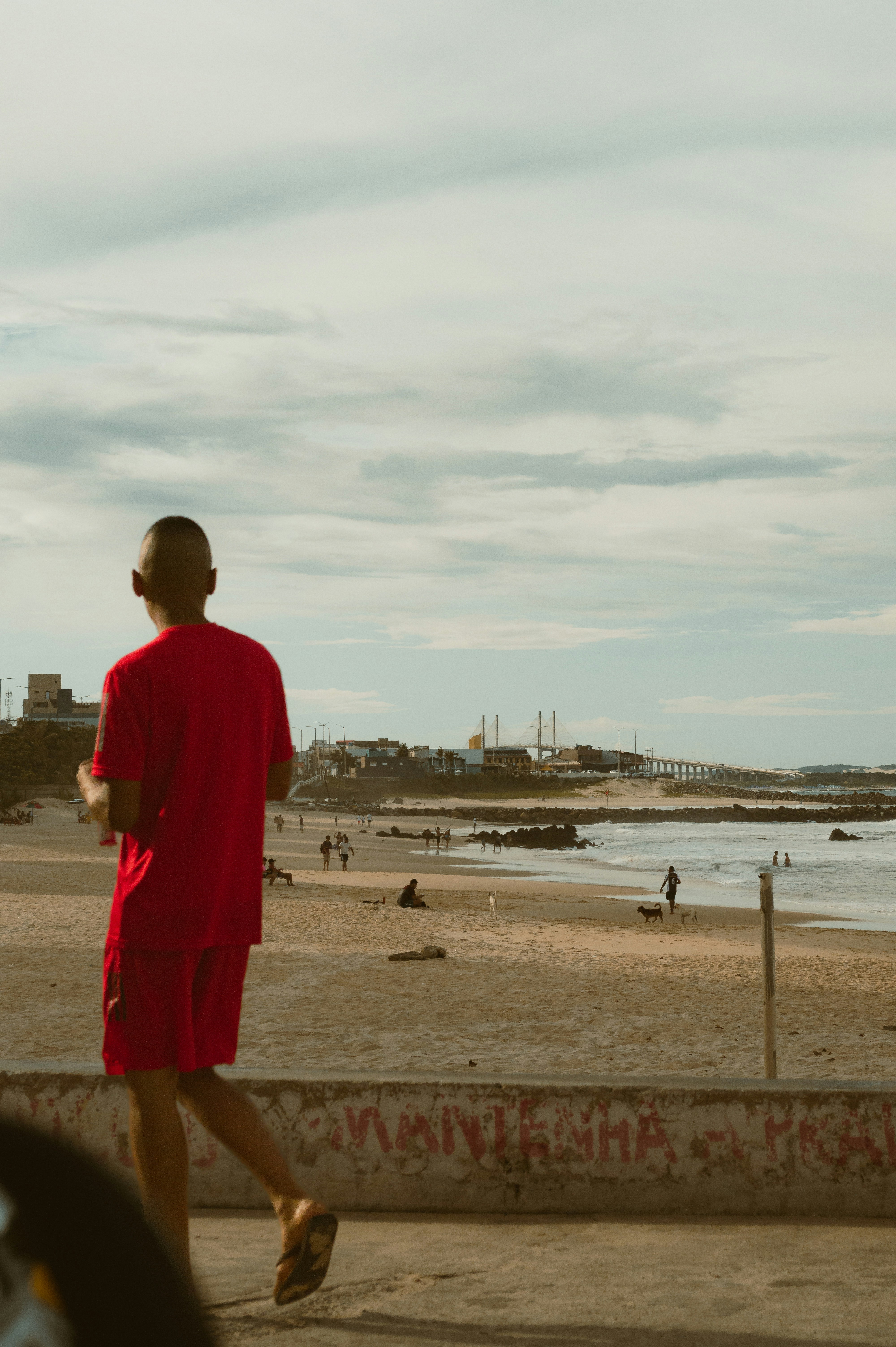 Red-clad jogger along sunlit beach with distant breakwater