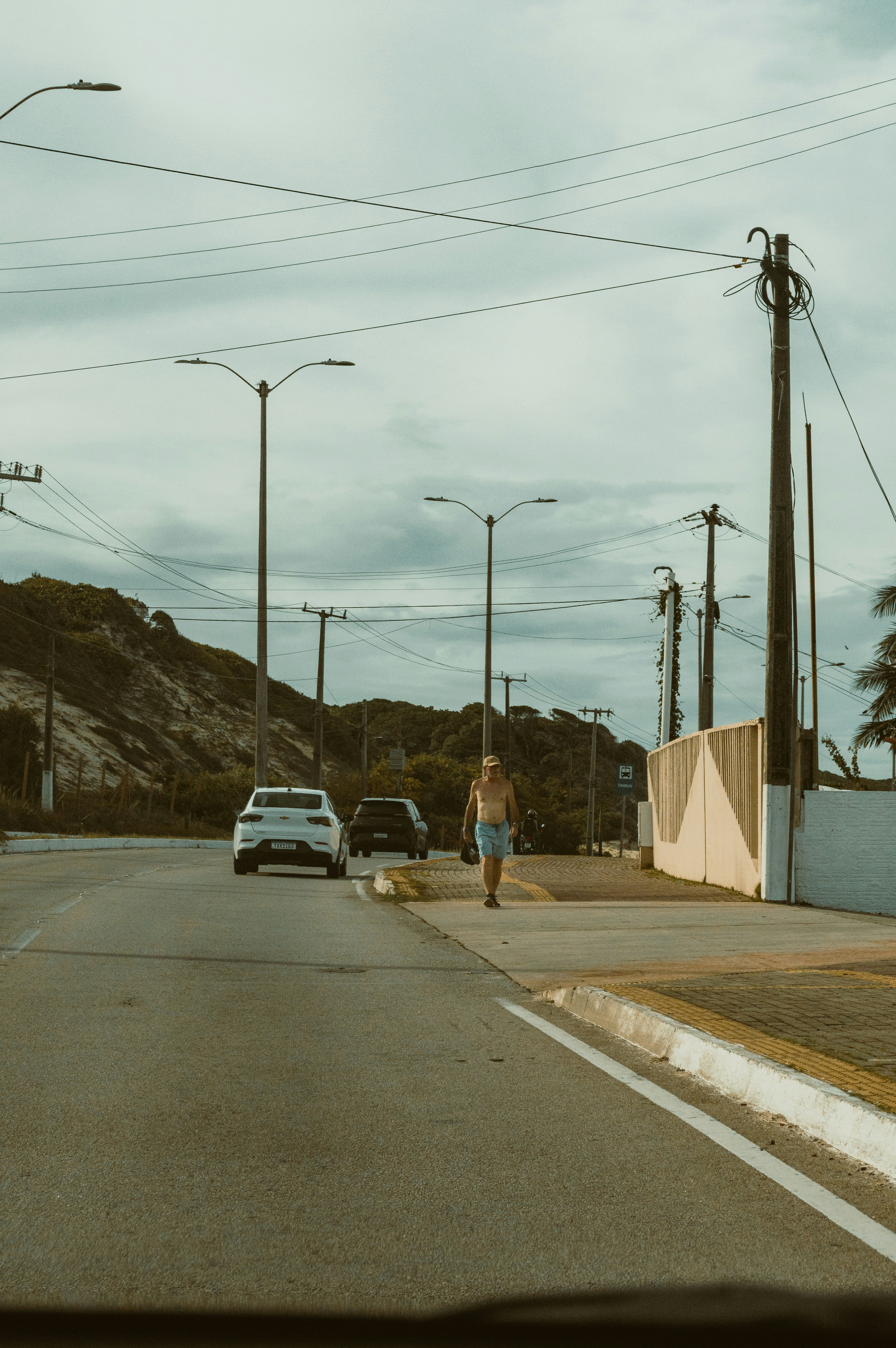 Sunlit Walk: A lone figure crosses a quiet coastal street