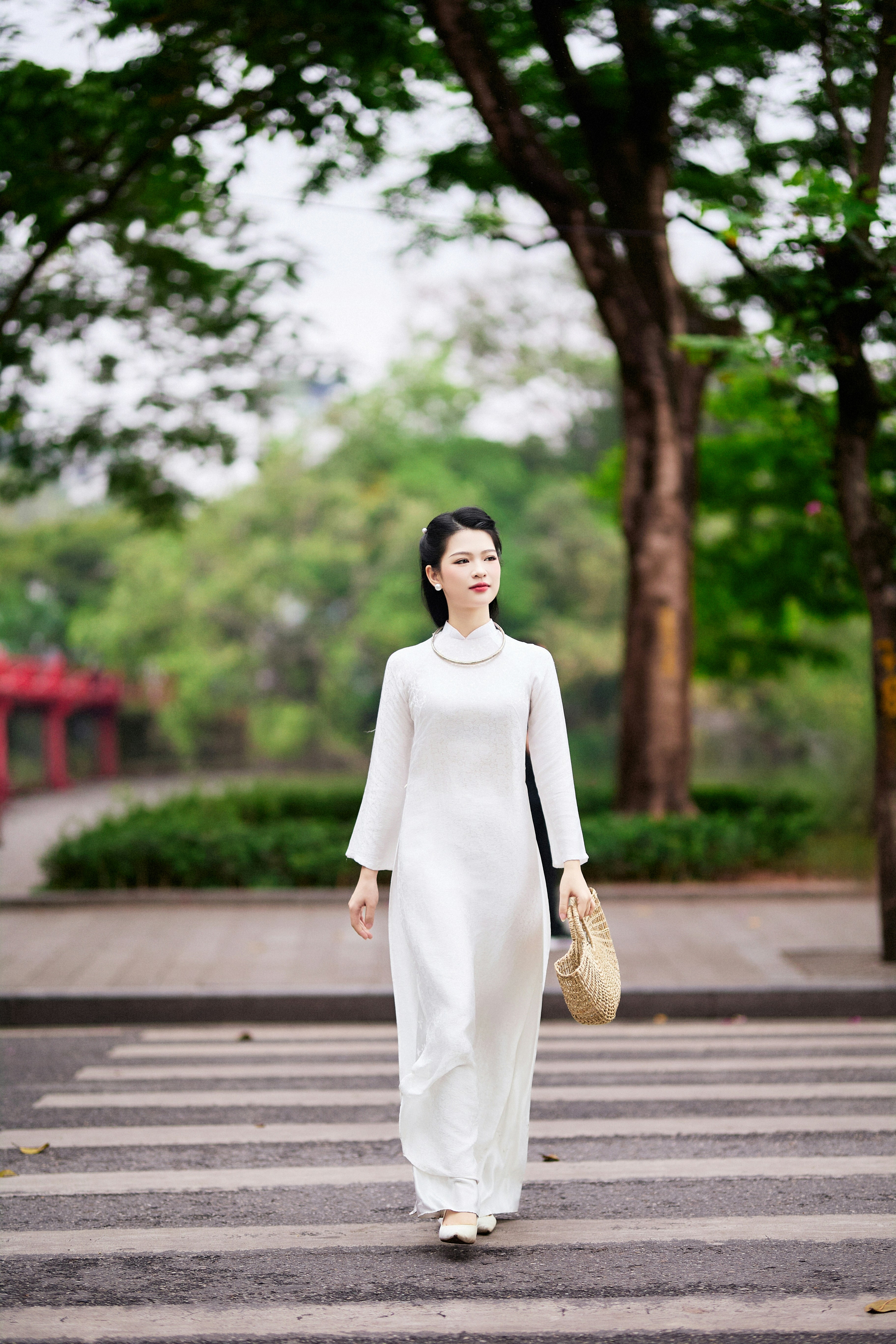 Elegant stride: a woman in a white ao dai crosses a city street