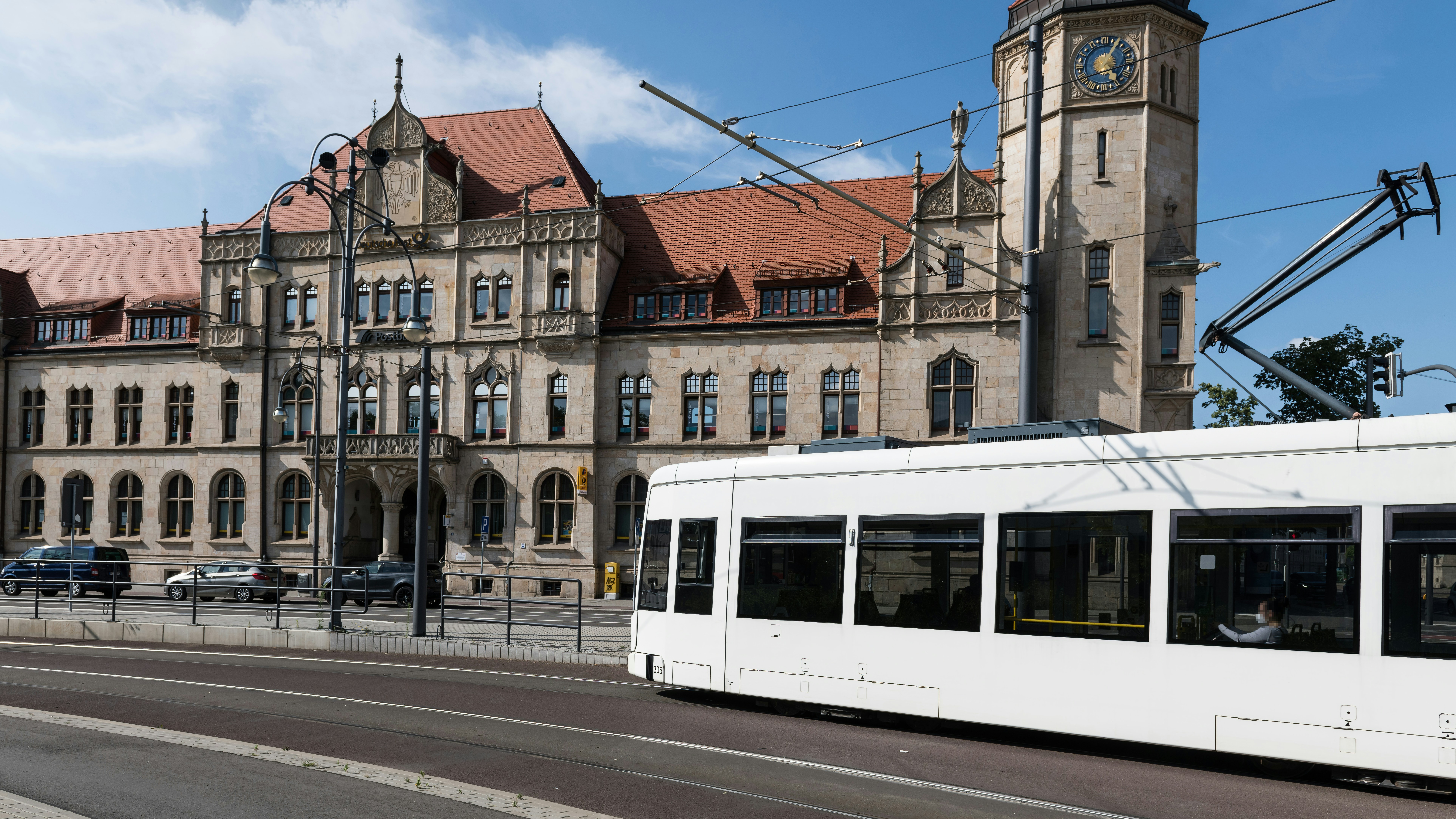 White tram gliding past a historic stone building with a clock tower