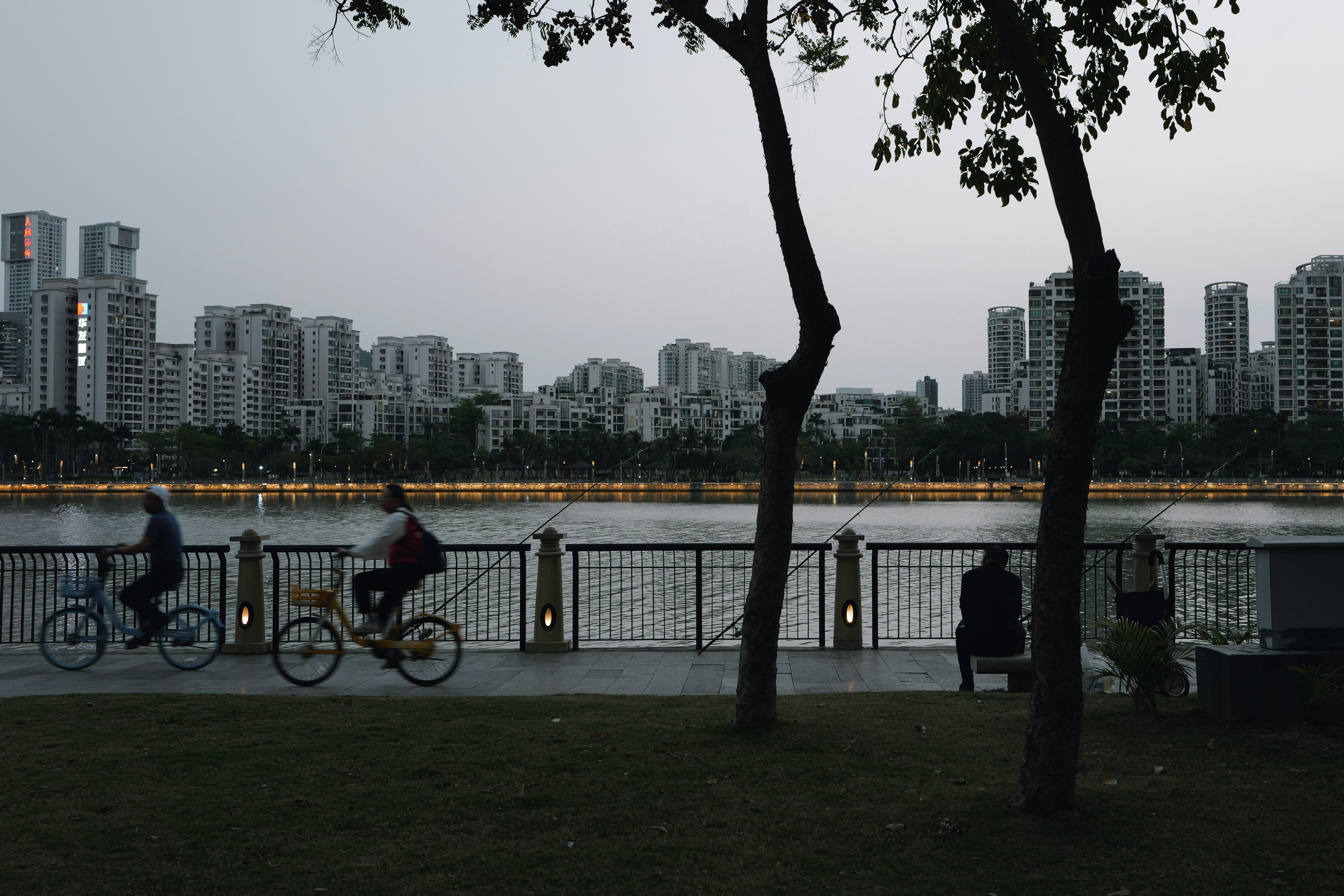 Riverfront in Dusk: Cyclists and Skyline Silhouettes