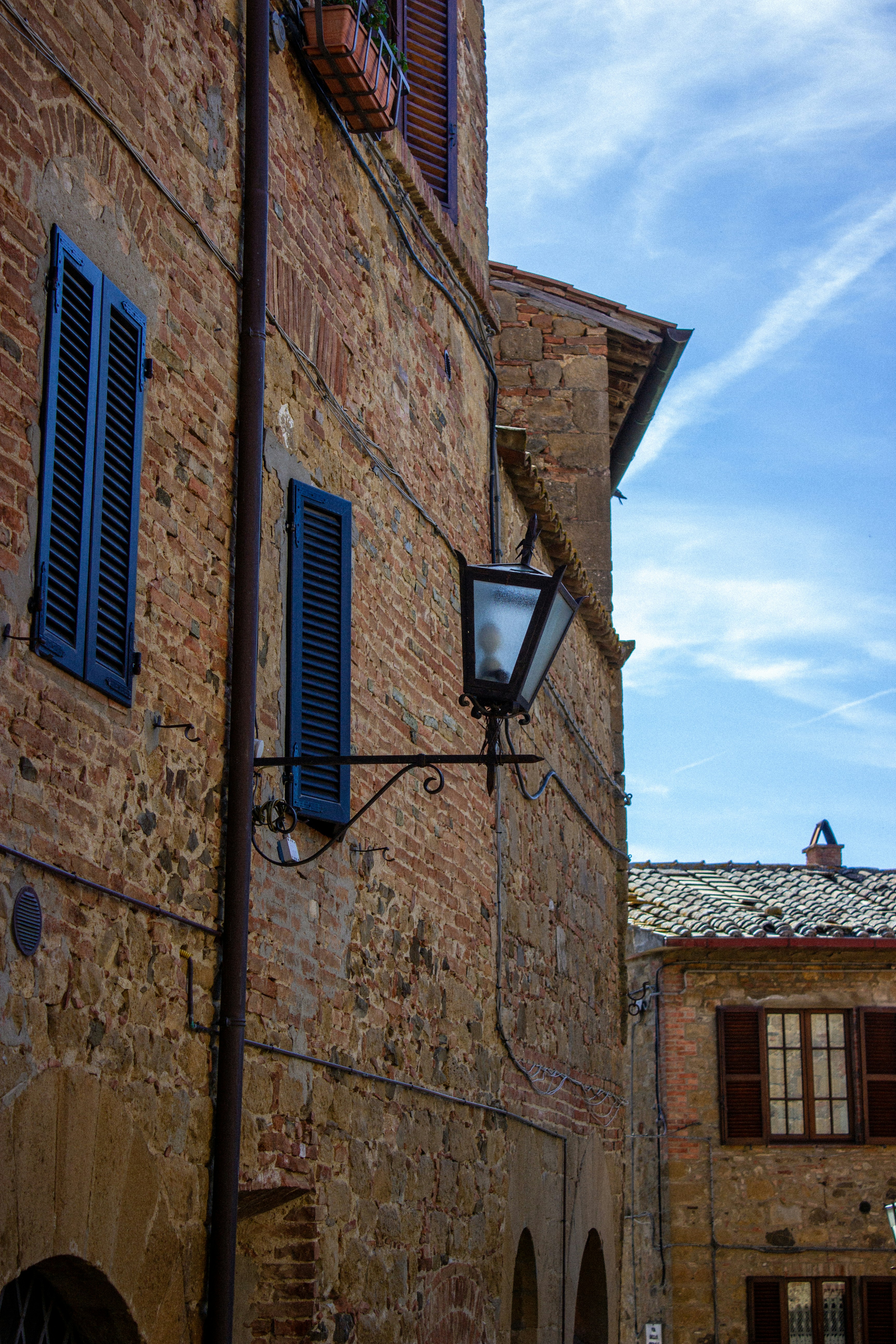 Blue shutters on sunlit stone: a Tuscan street under a bright sky