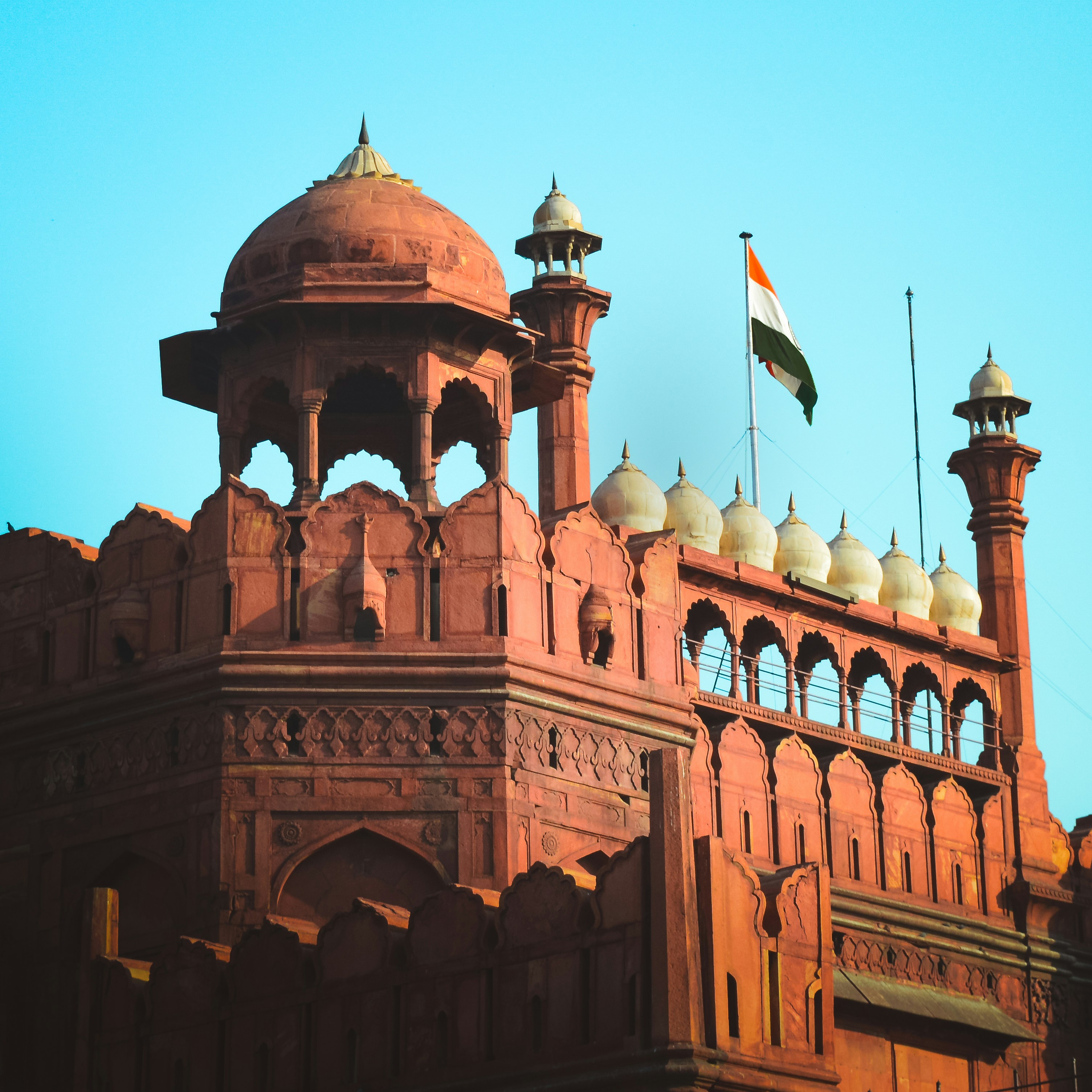 Red sandstone pavilion under a bright Indian sky with a fluttering flag