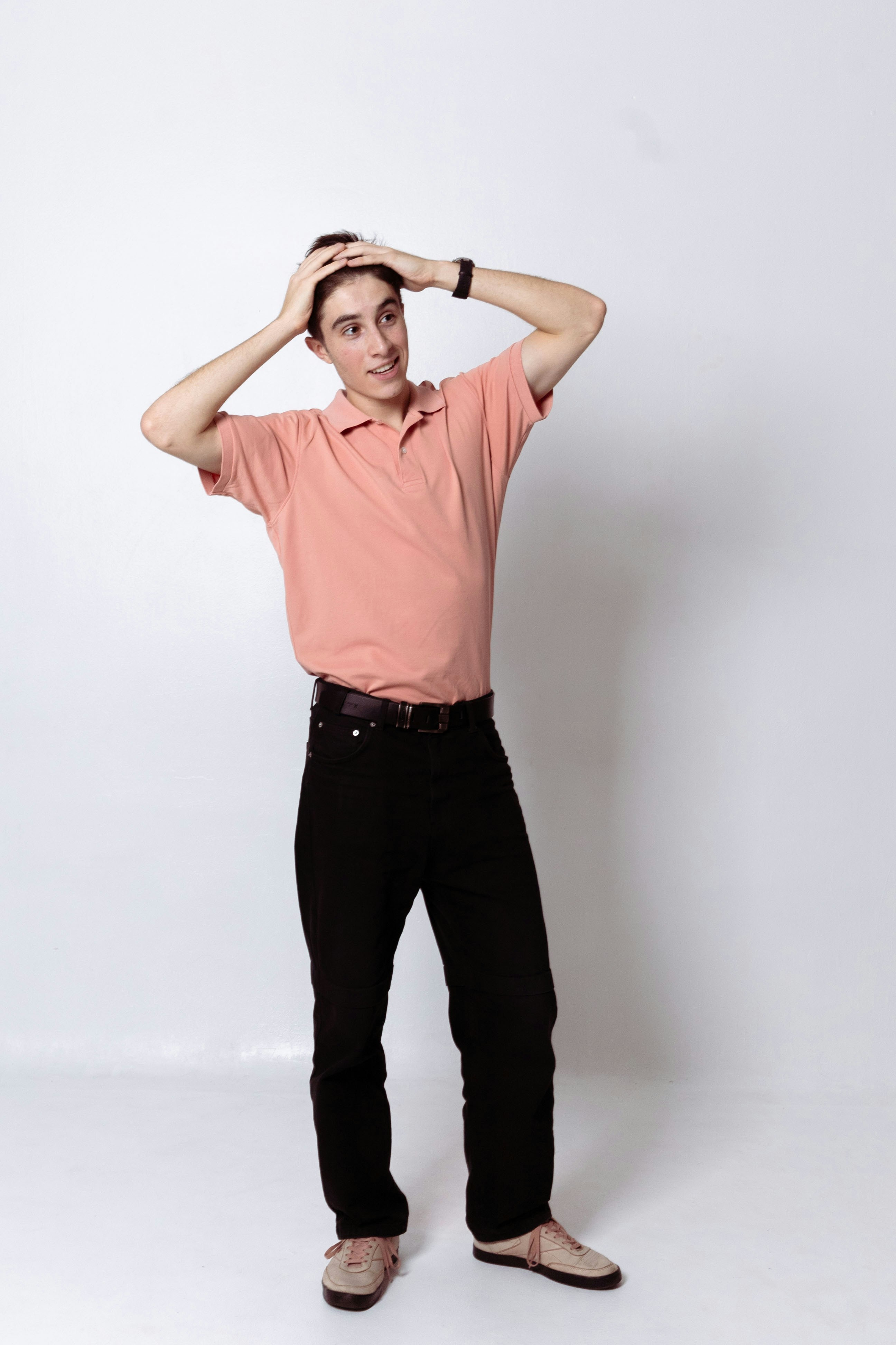 Casual Confidence: A man in peach polo poses with hands in hair against a clean studio backdrop
