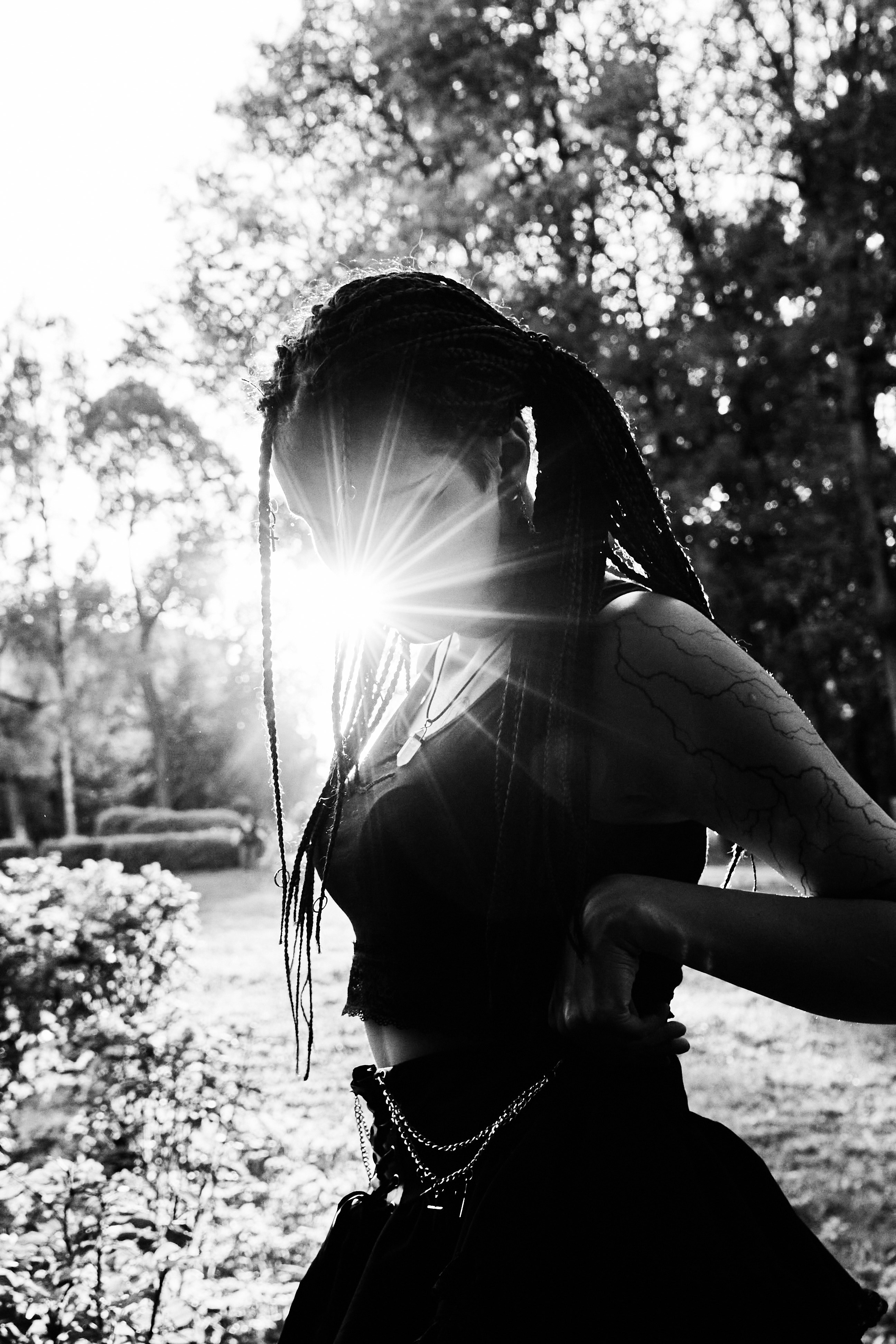 Sunlit silhouette: a dancer in black, braided shadows in a park