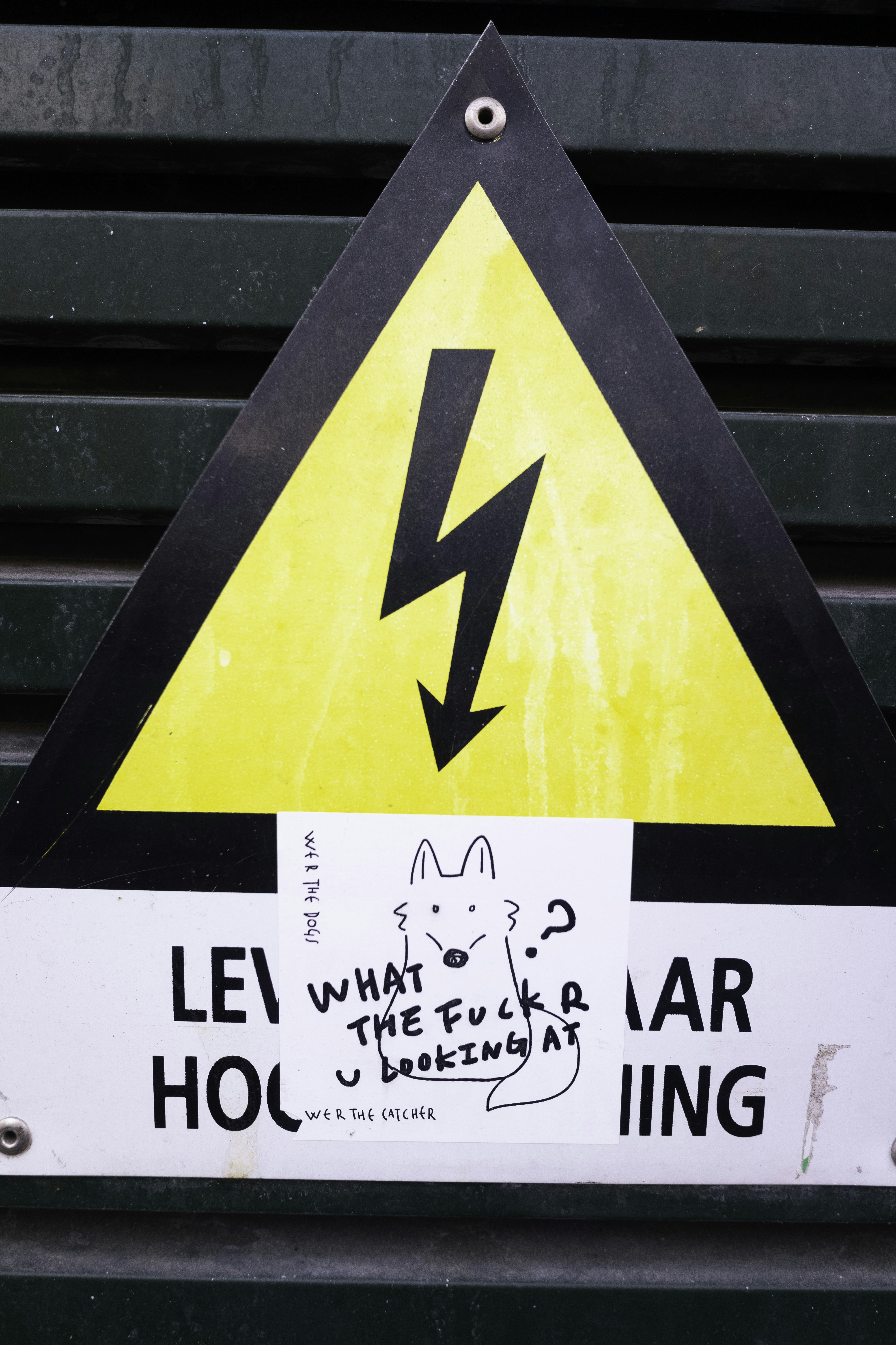 Warning Sign with Graffiti Note: A Subversive Sticker on the Triangle