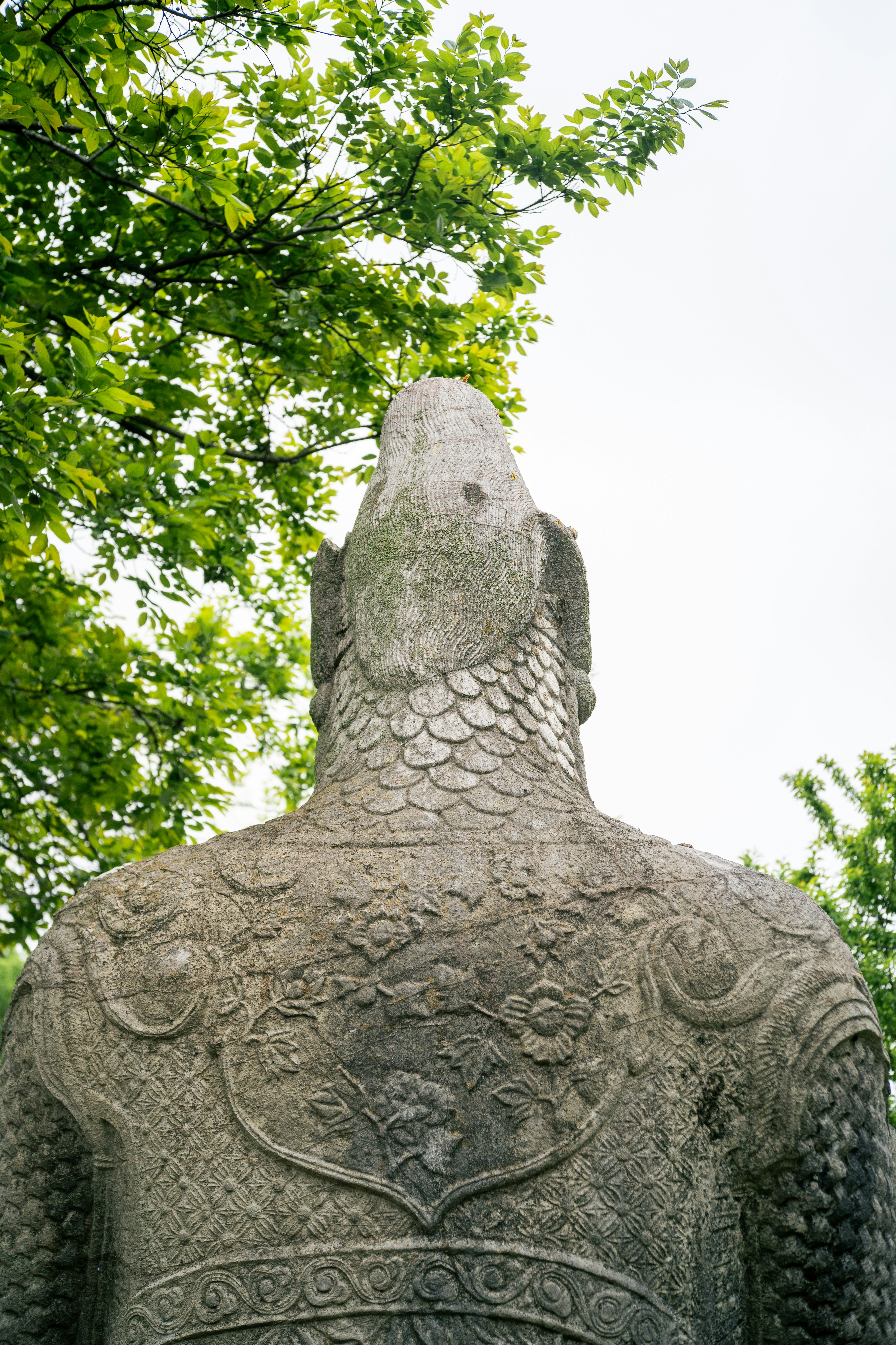 Carved Guardian: A Stone Dragon-Like Armor Statue Surrounded by Green Canopy